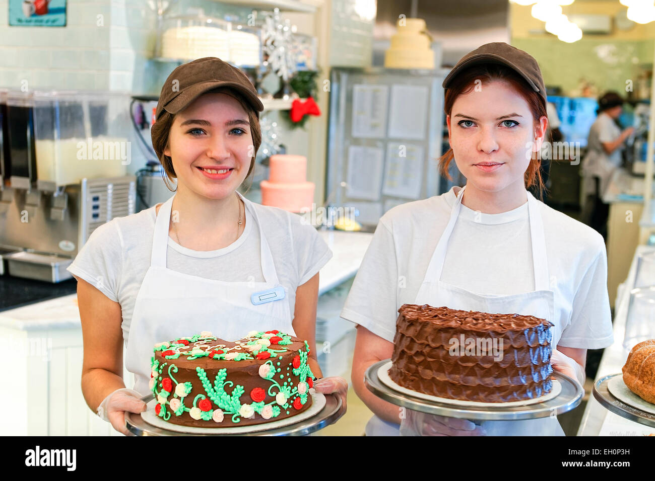 Two young girls with chocolate decorated cakes at the bakery counter ...