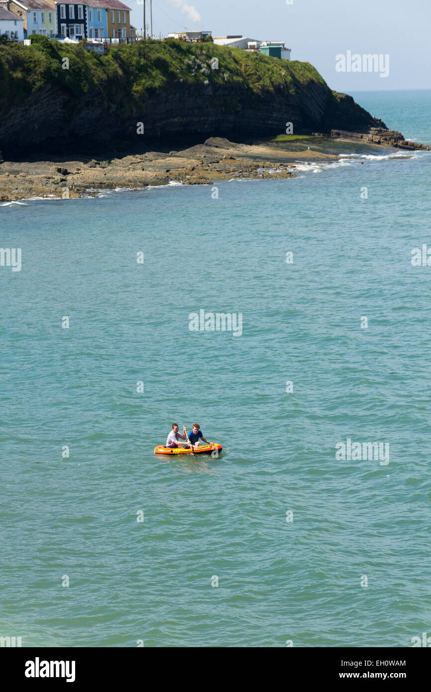 Small inflatable boat being paddled by two young men a little way off ...