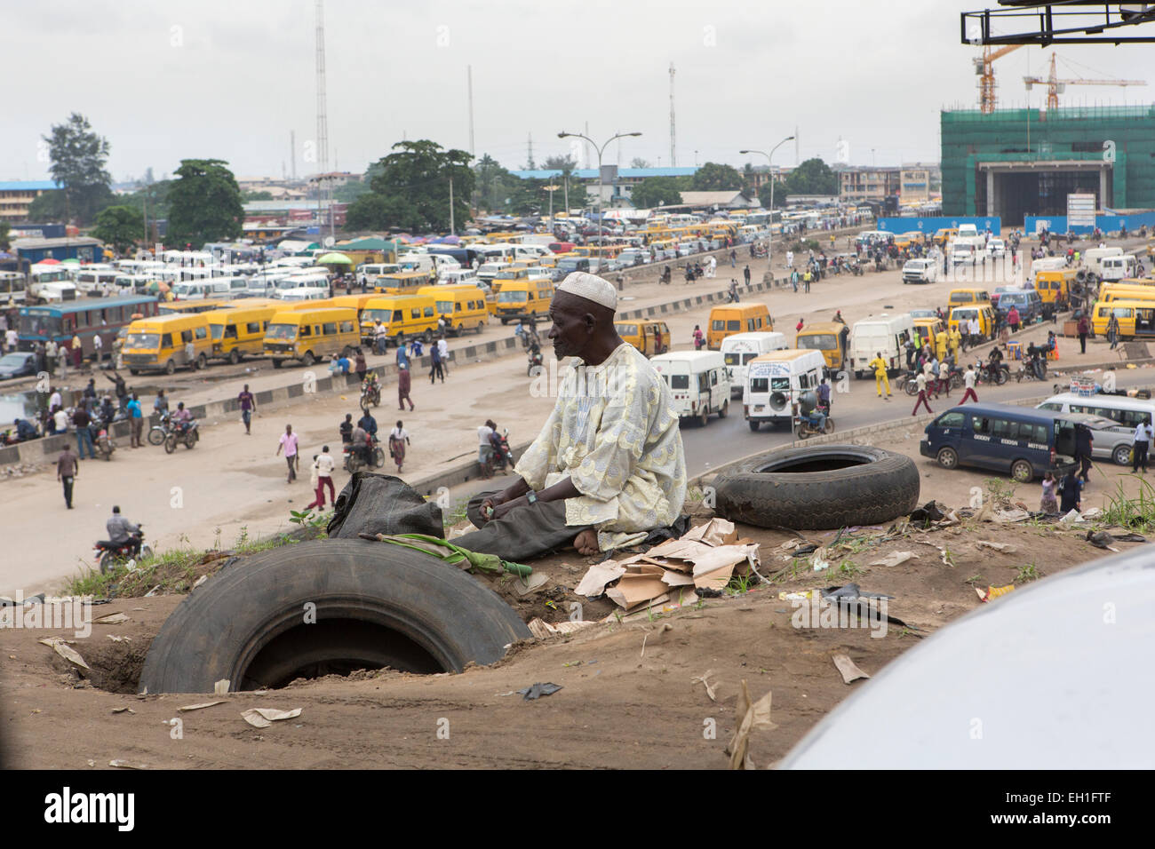 Lagos, Nigeria; On old man sits by the roadside overlooking a bus ...