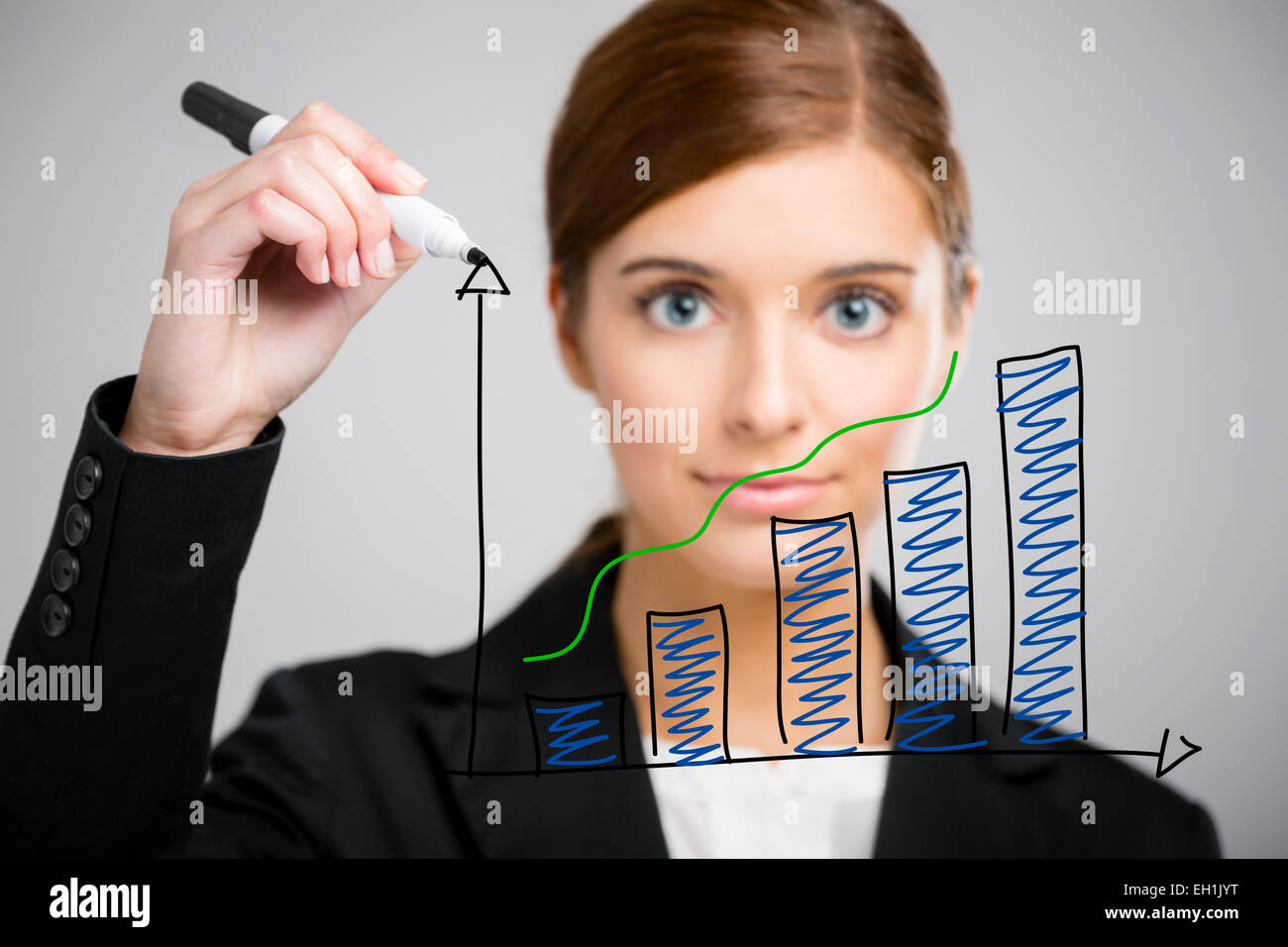 Beautiful businesswoman drawing a chart on a glass board with a marker ...