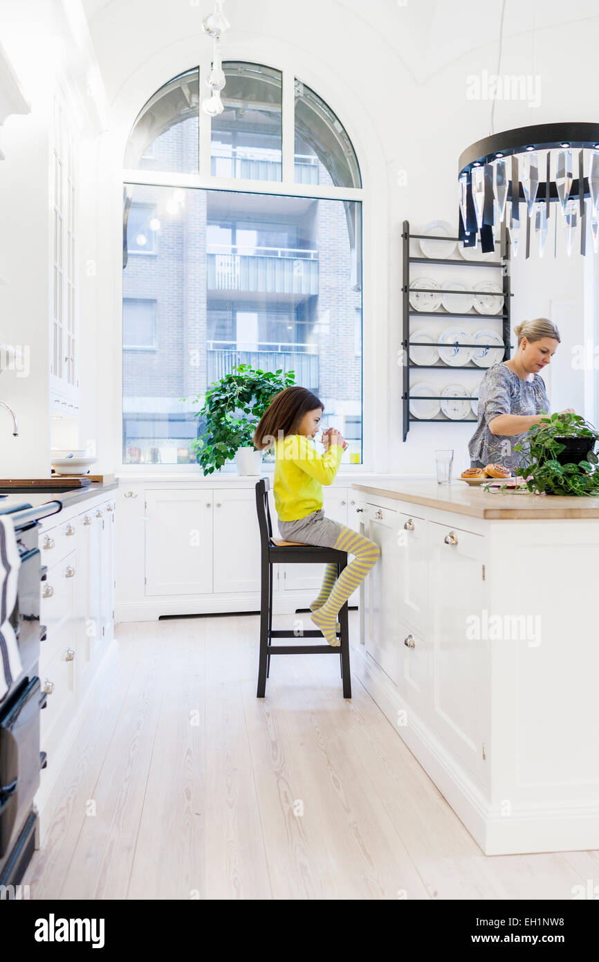 Girl drinking juice while mother cooking in kitchen Stock Photo - Alamy