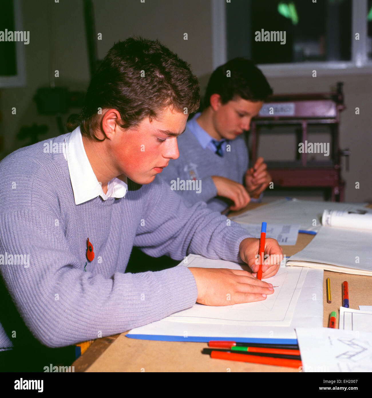 Teenage boy writing with pen in his notebook in school classroom at ...