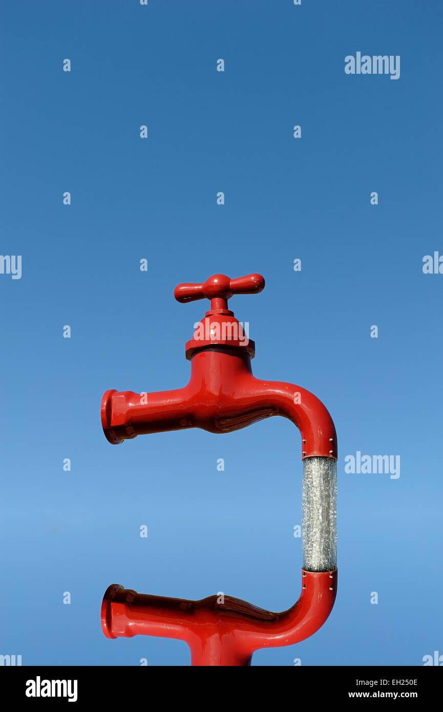 A red industrial running tap fountain set against a blue sky,digitally ...