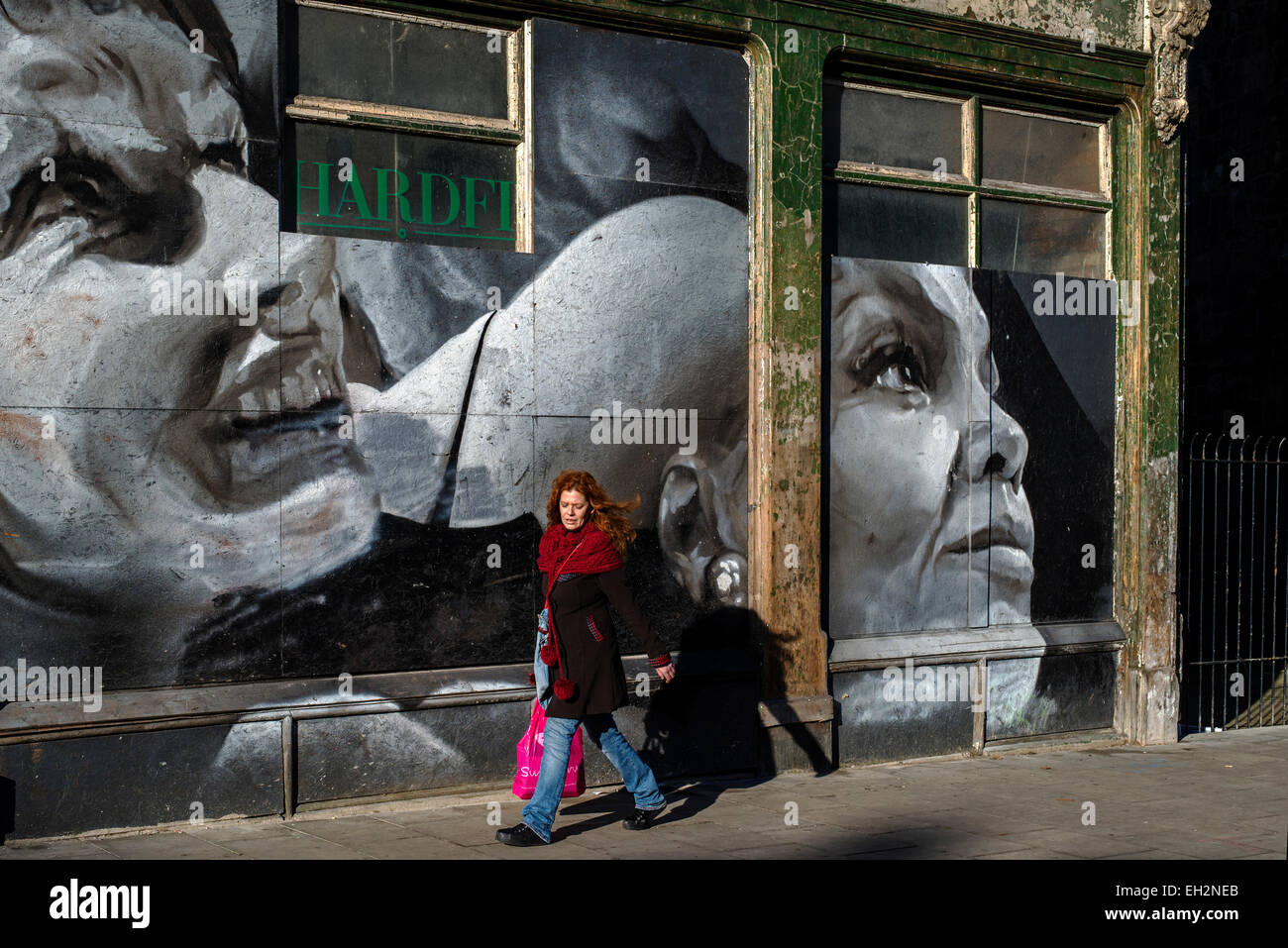 A young woman walks by graffiti portraits on a derelict store on Leith ...