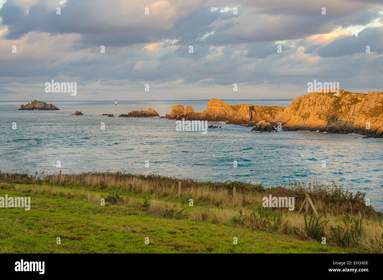 Cliffs with lighthouse in the distance, with rocks illuminated by sun ...