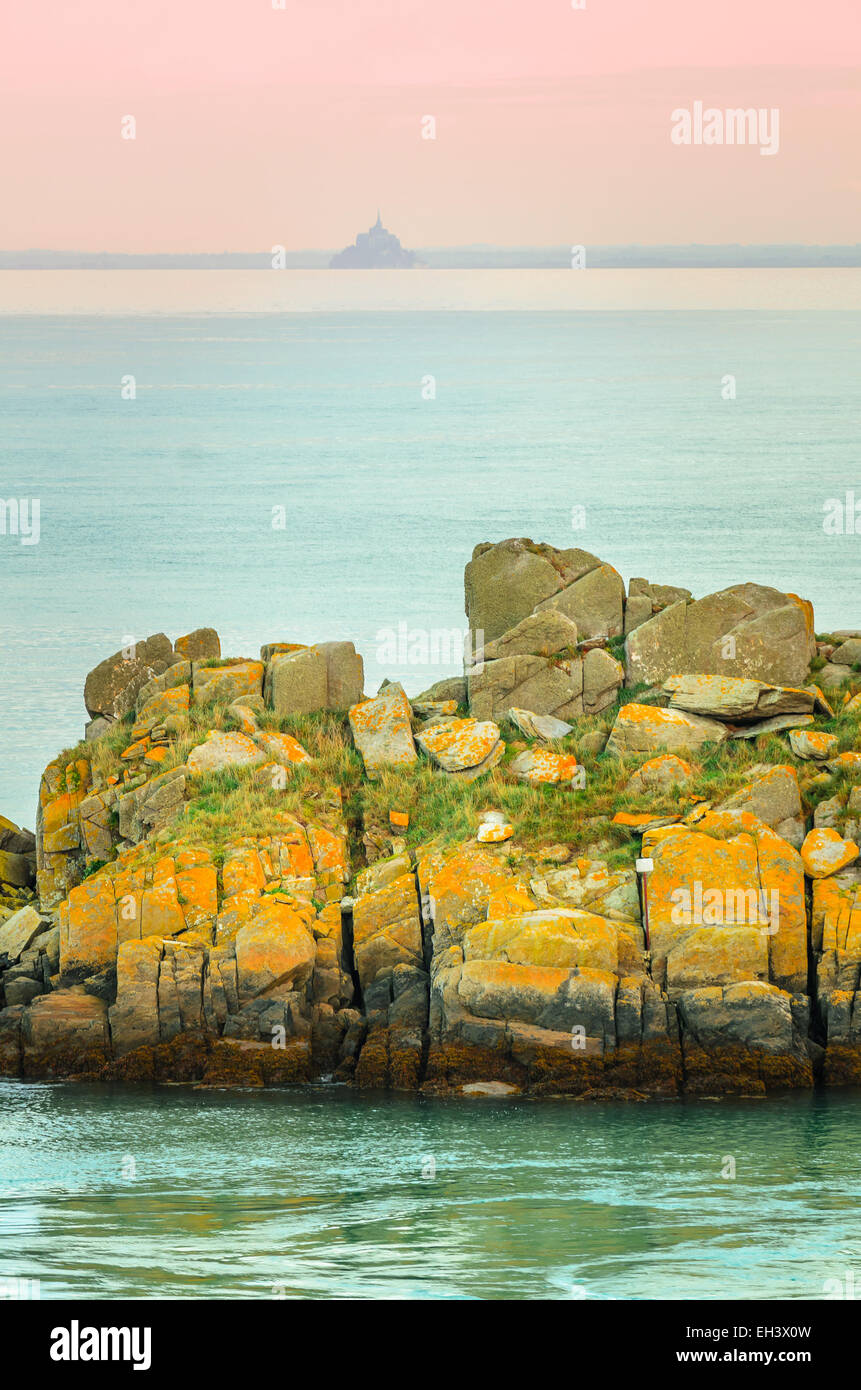 Yellow rocks on French coast with silhouette of Mont Saint Michel in ...