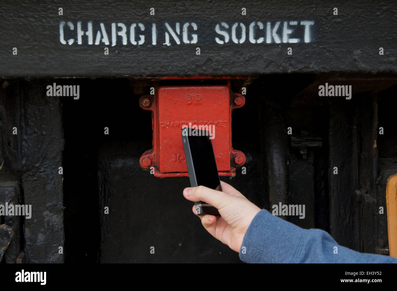 Phone Held Up In Humour Next To Sign Saying Charging Socket Under A phone-held-up-in-humour-next-to-sign-saying-charging-socket-under-a