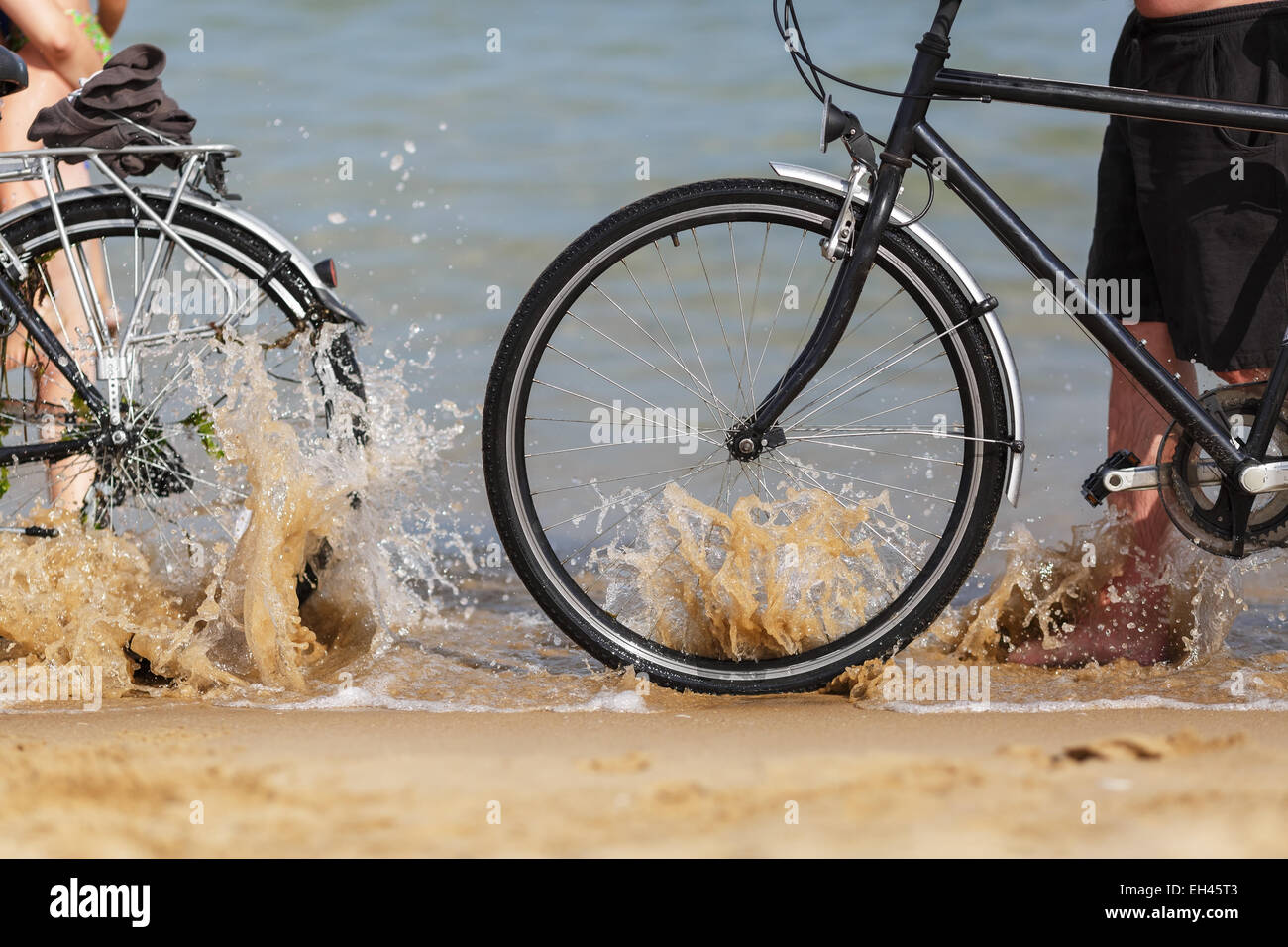 Sea wave splashing on the wheels of two bikes on the beach. Shallow ...