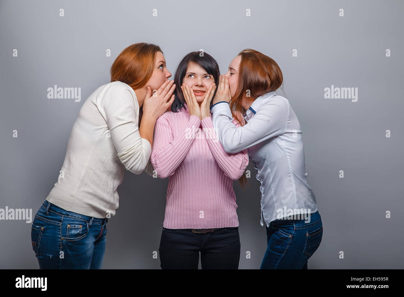 two girls in jeans European appearance whisper in the ear of the third ...