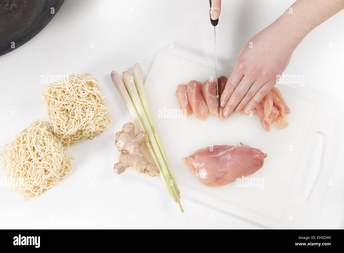Young woman in a white kitchen making a chicken meat fillet dish with ...