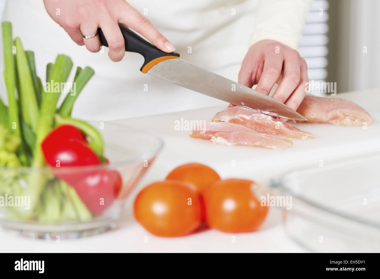 Young woman in a white kitchen making a chicken meat fillet dish Stock ...