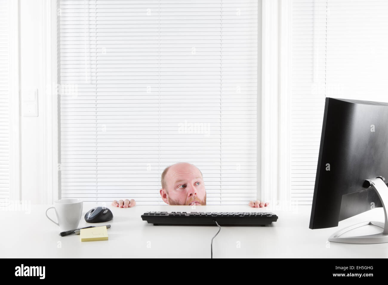 Office worker threatened or scared by the computer. Hiding behind his ...