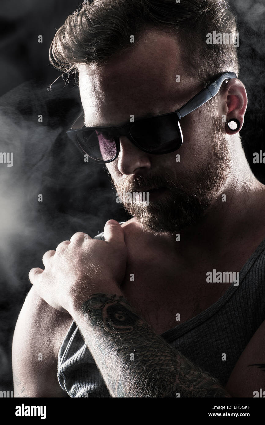 Young man / rocker with sunglasses, tattoos and ear rings. Smoke and ...
