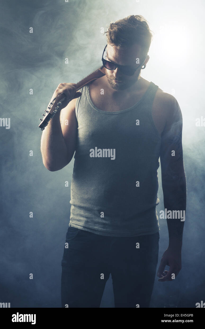 Young man / rocker with guitar and sunglasses. Smoke and scene light ...