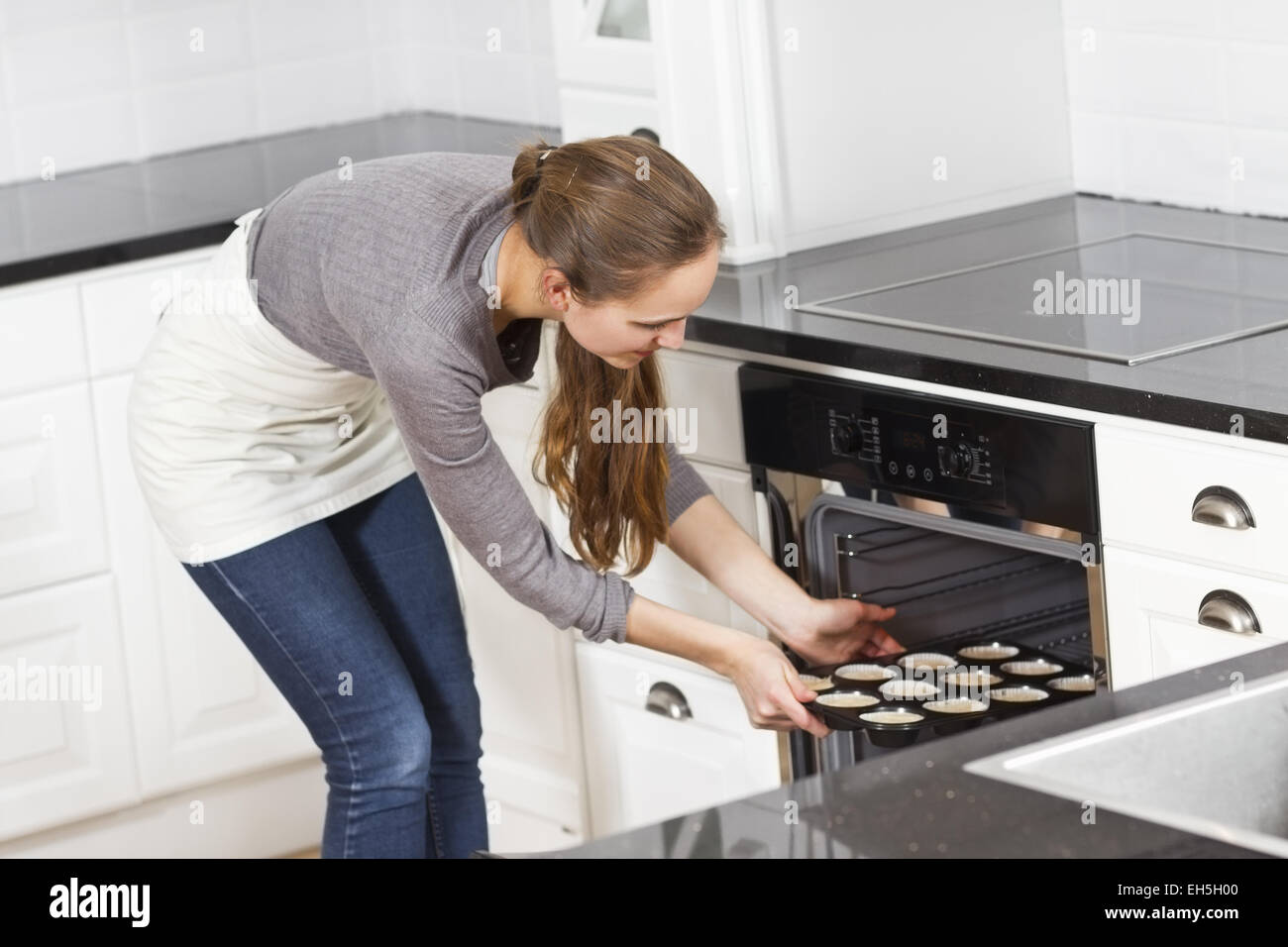 A woman making / baking muffins in white kitchen modern kitchen Stock ...