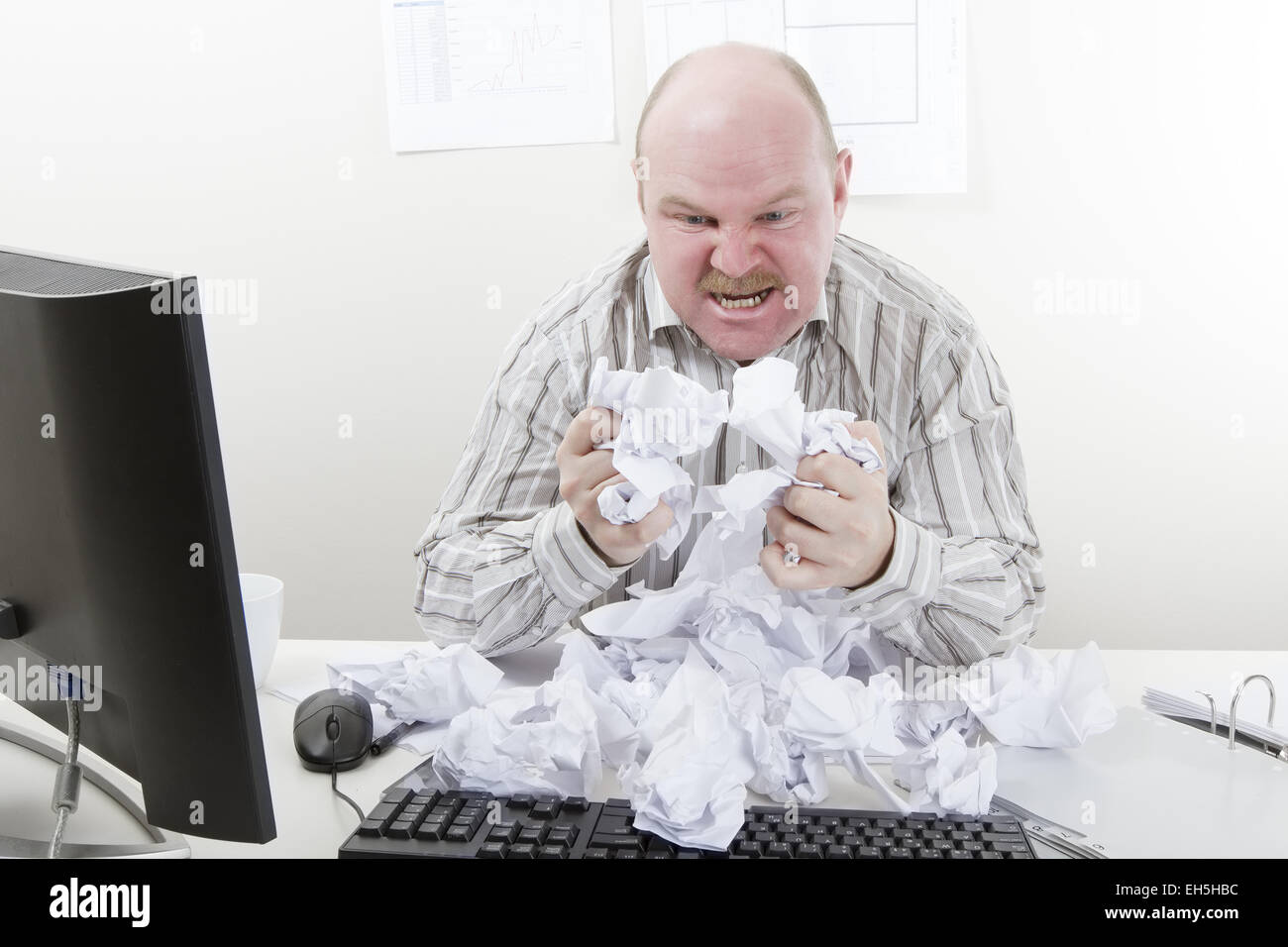 Angry and overworked office worker with a heap of paper at the office ...