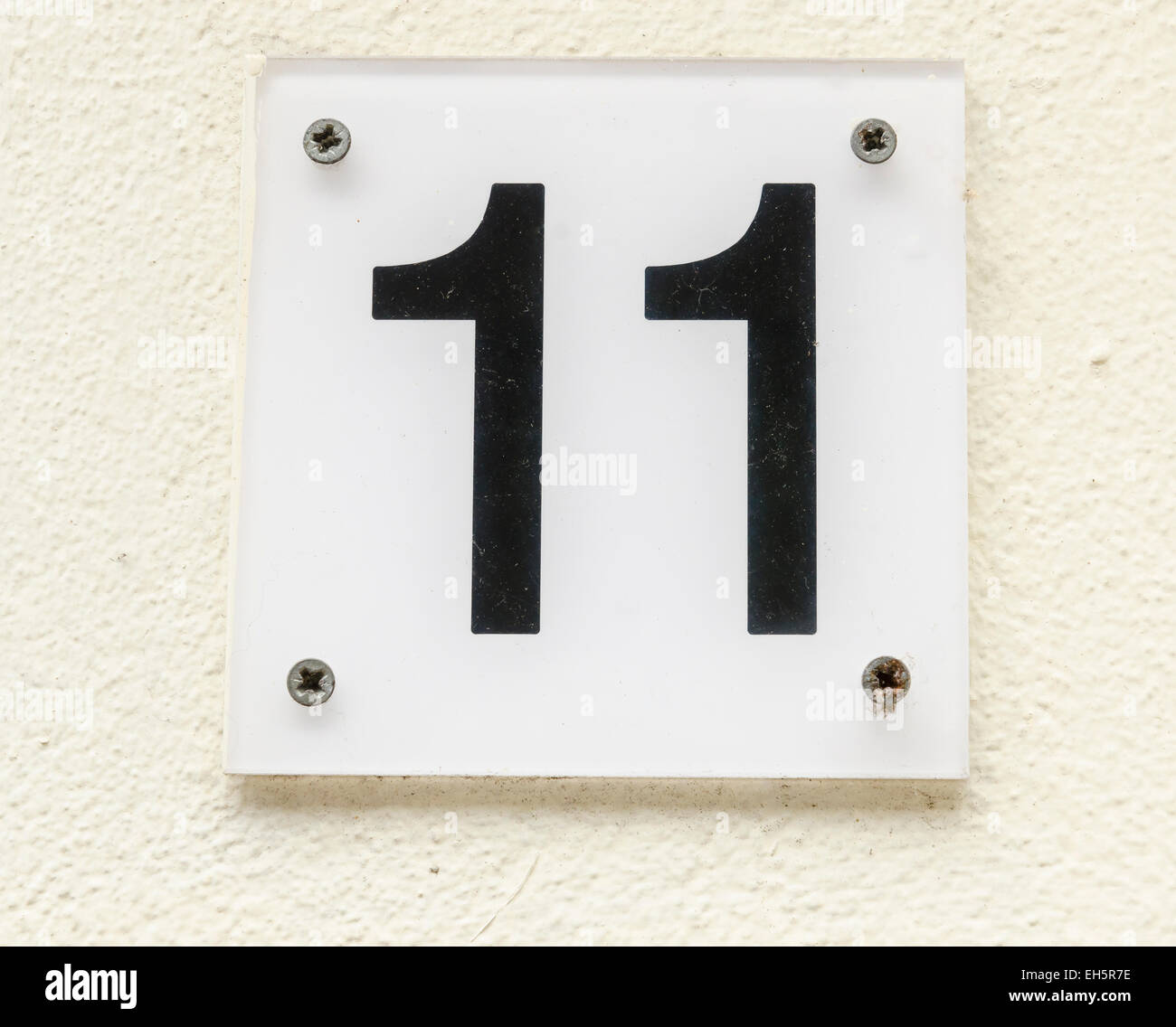 Sign of house number 11 in black characters on a white yellowish wall ...