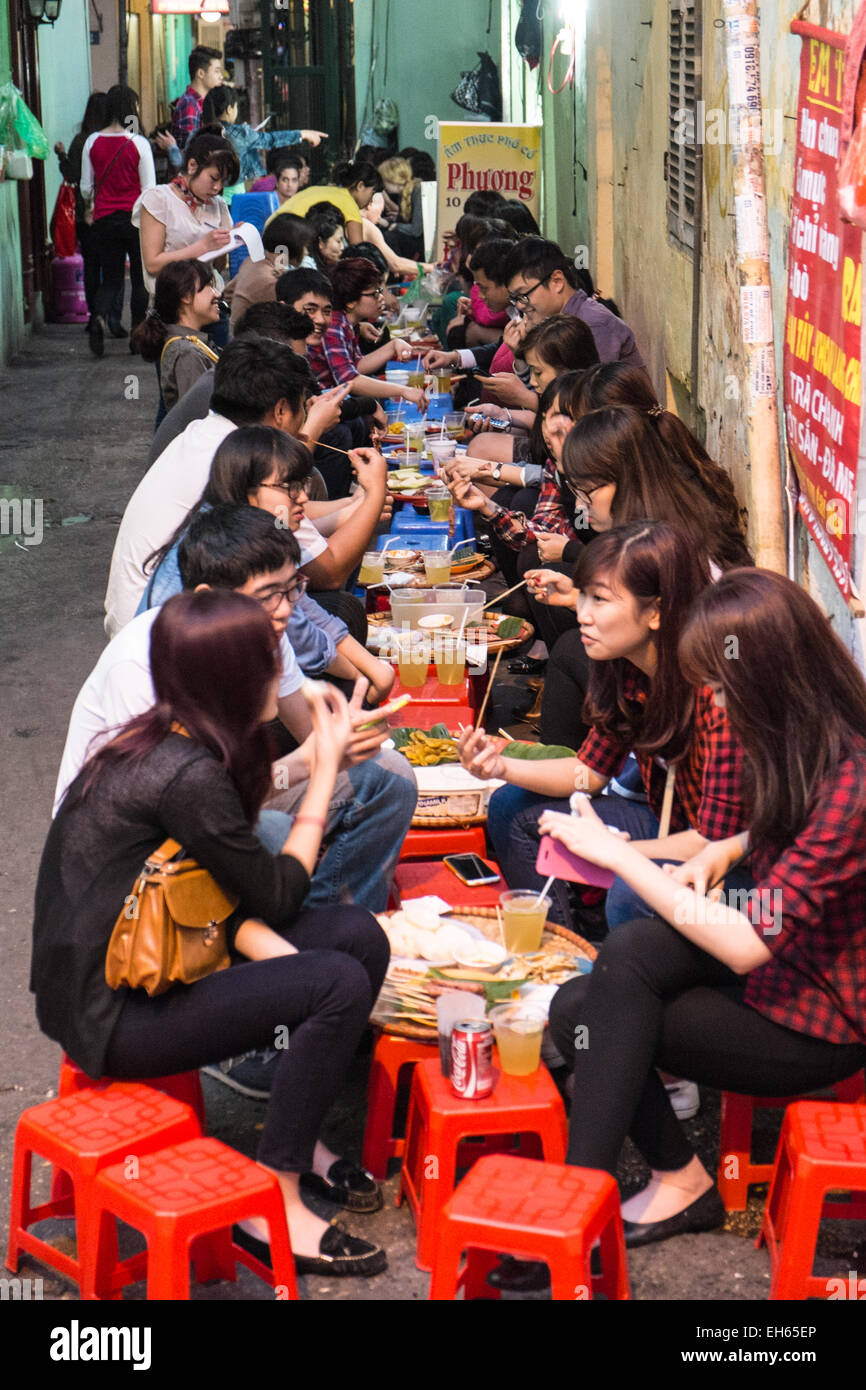 Young sitting on stools eating street food in Old Quarter of Han Noi ...