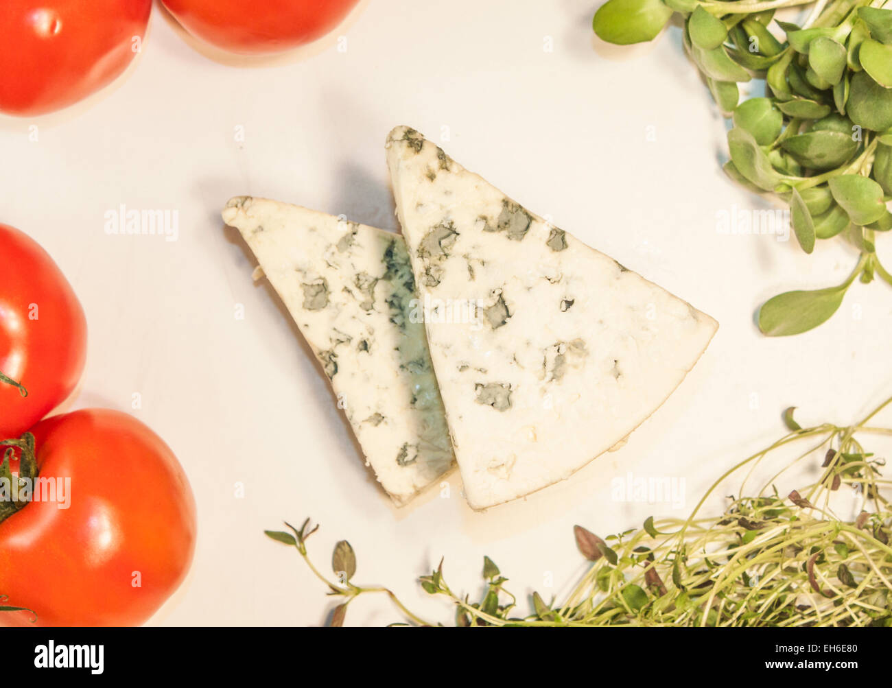 Two triangles of blue cheese, between herbs and tomatoes Stock Photo ...