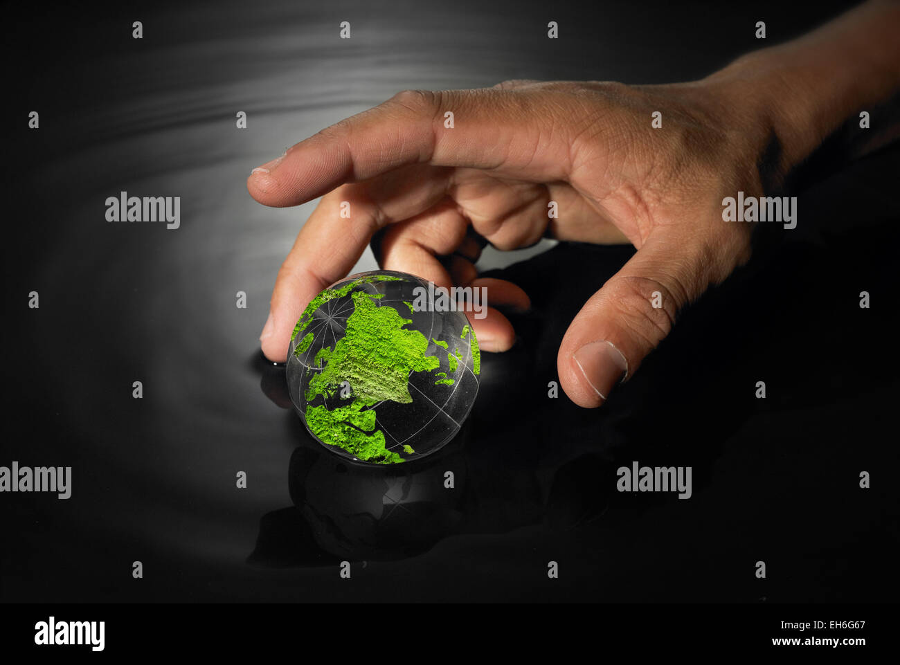 Hand reaching for crystal earth ball with water wave black background ...