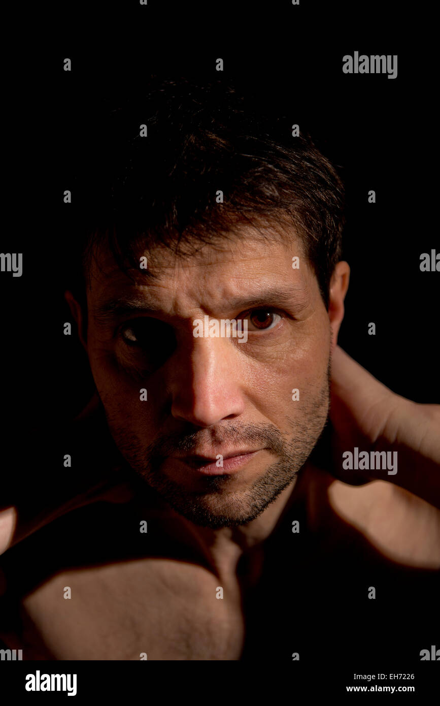 Upset looking man, with half his face in shadow against a black ...