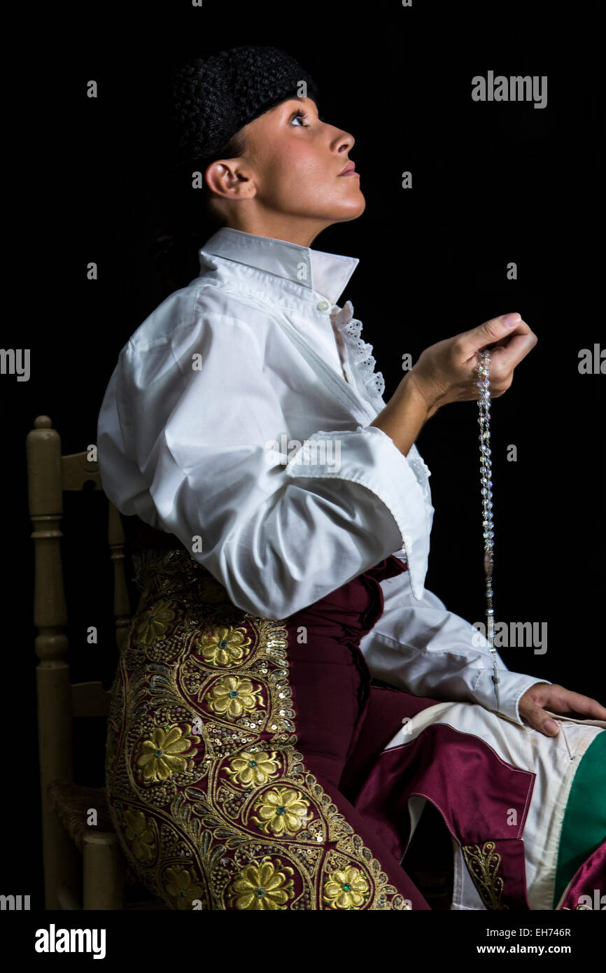 Woman Bullfighter in Chapel praying with Rosary on her hand on a black ...