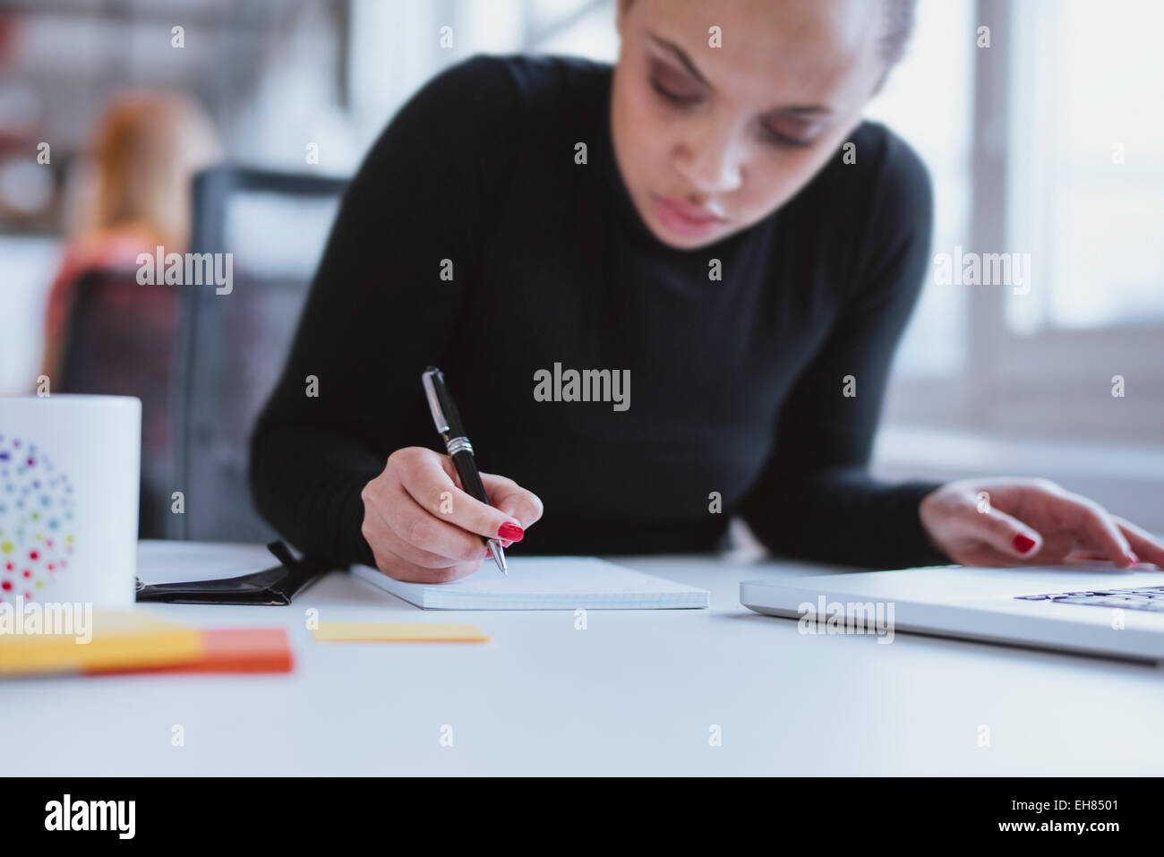Young woman working at her desk taking notes. Focus on hand writing on ...