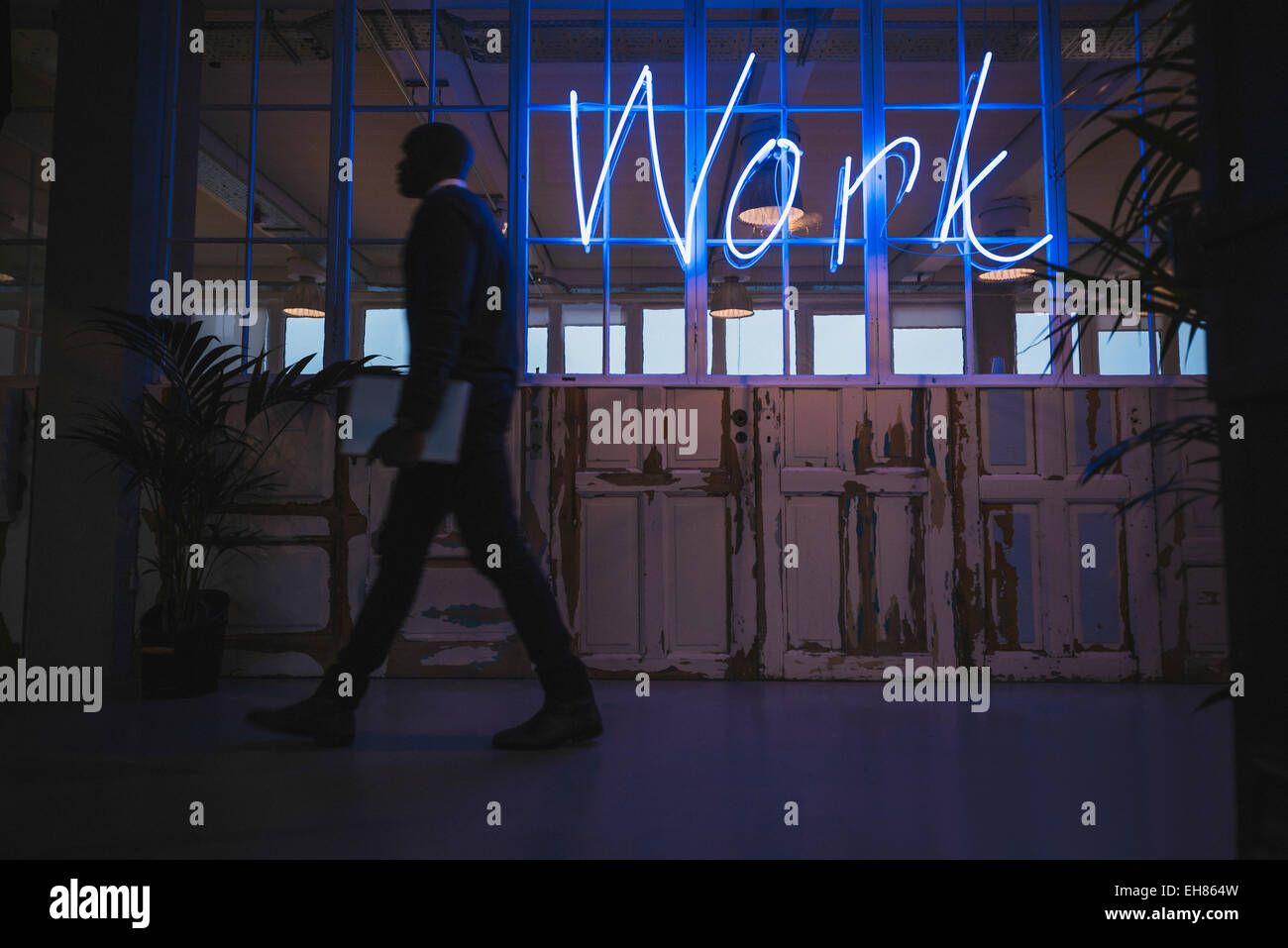 Corridor of a modern office with a neon work sign and executive walking ...