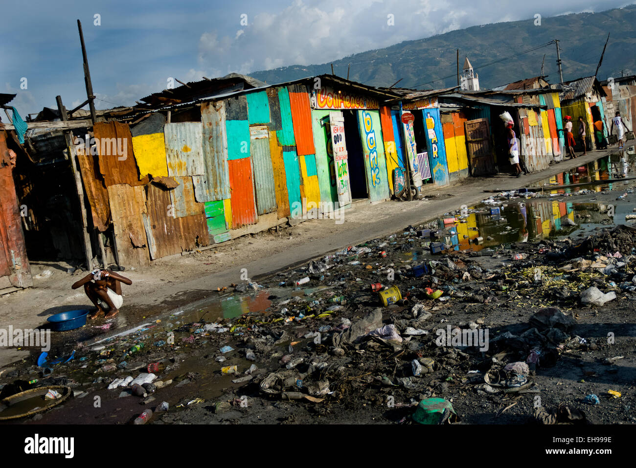 A Haitian woman bathes in a bucket outside sheet-metal houses in a ...