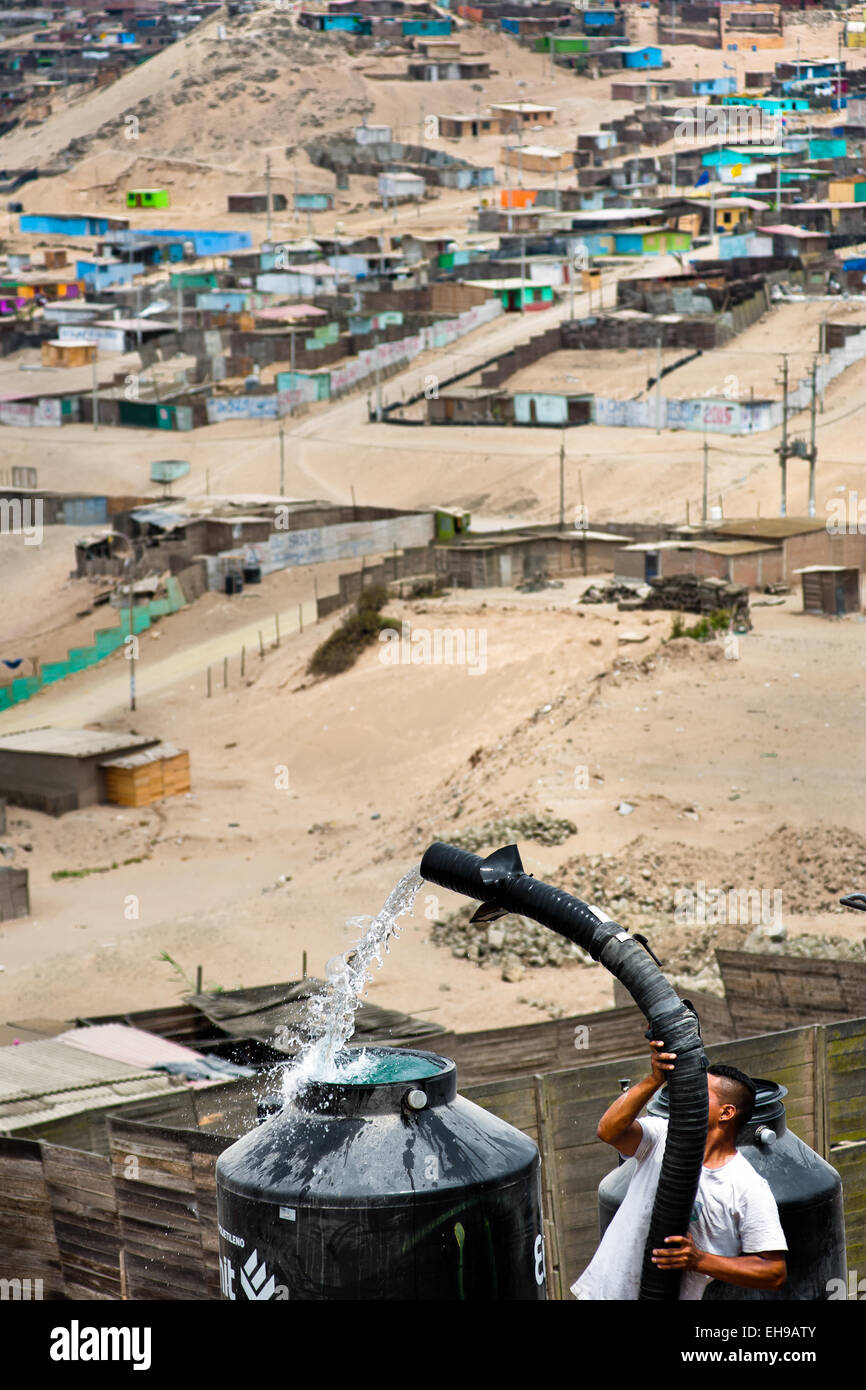 A Peruvian water distribution worker with a pipe fills a tank with ...