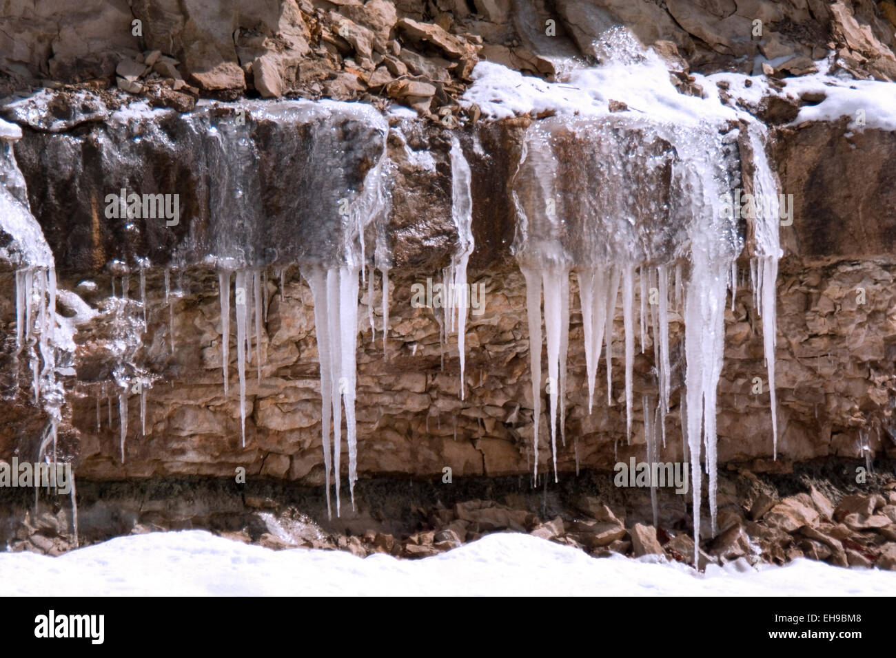 Icicles flow down over exposed layers of earth and stone Stock Photo ...