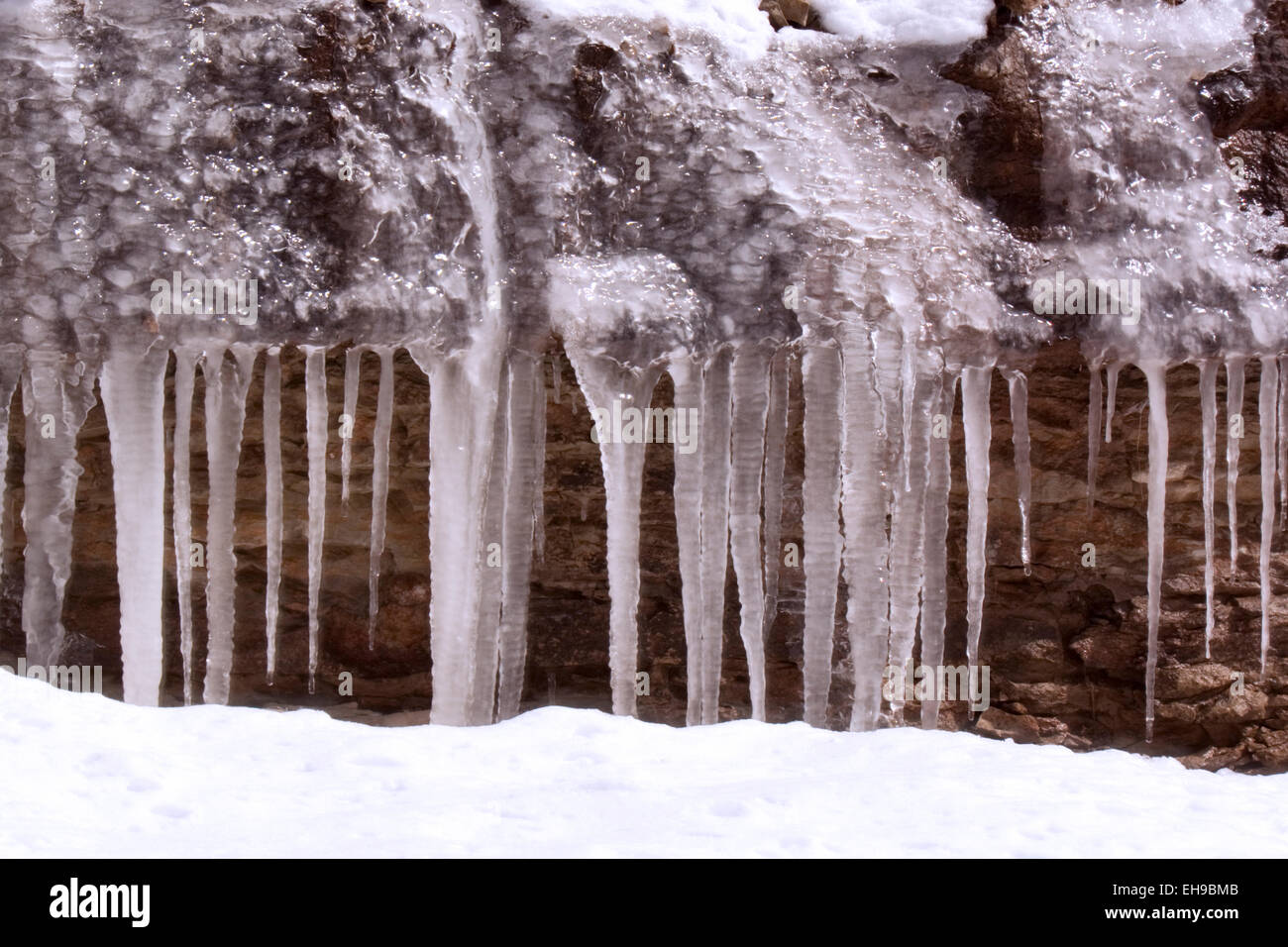Icicles flow down over exposed layers of earth and stone Stock Photo ...