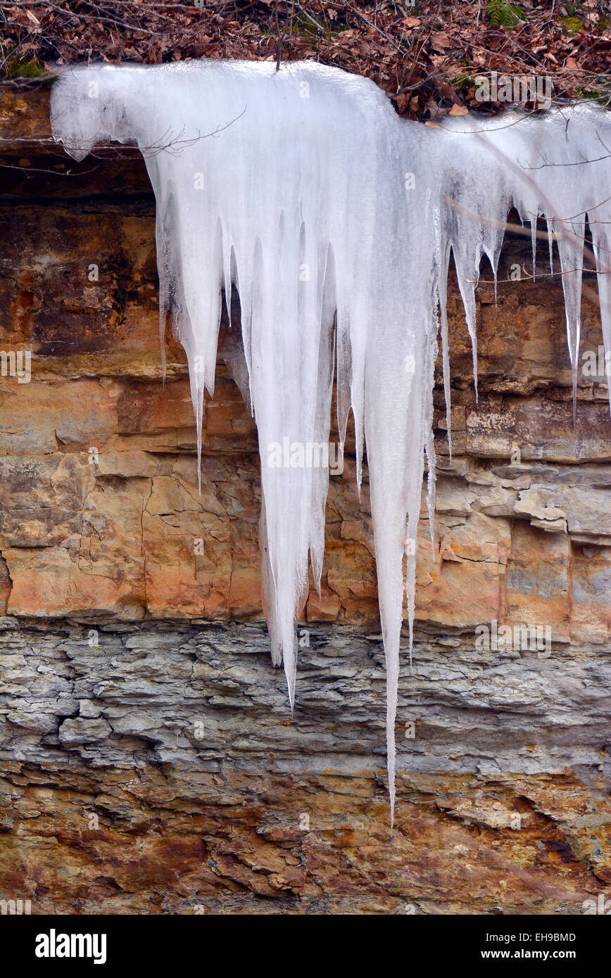 Icicles flow down over exposed layers of earth and stone Stock Photo ...