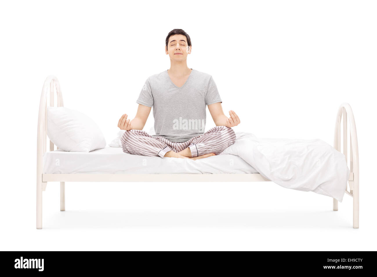 Calm guy meditating seated on bed isolated on white background Stock ...