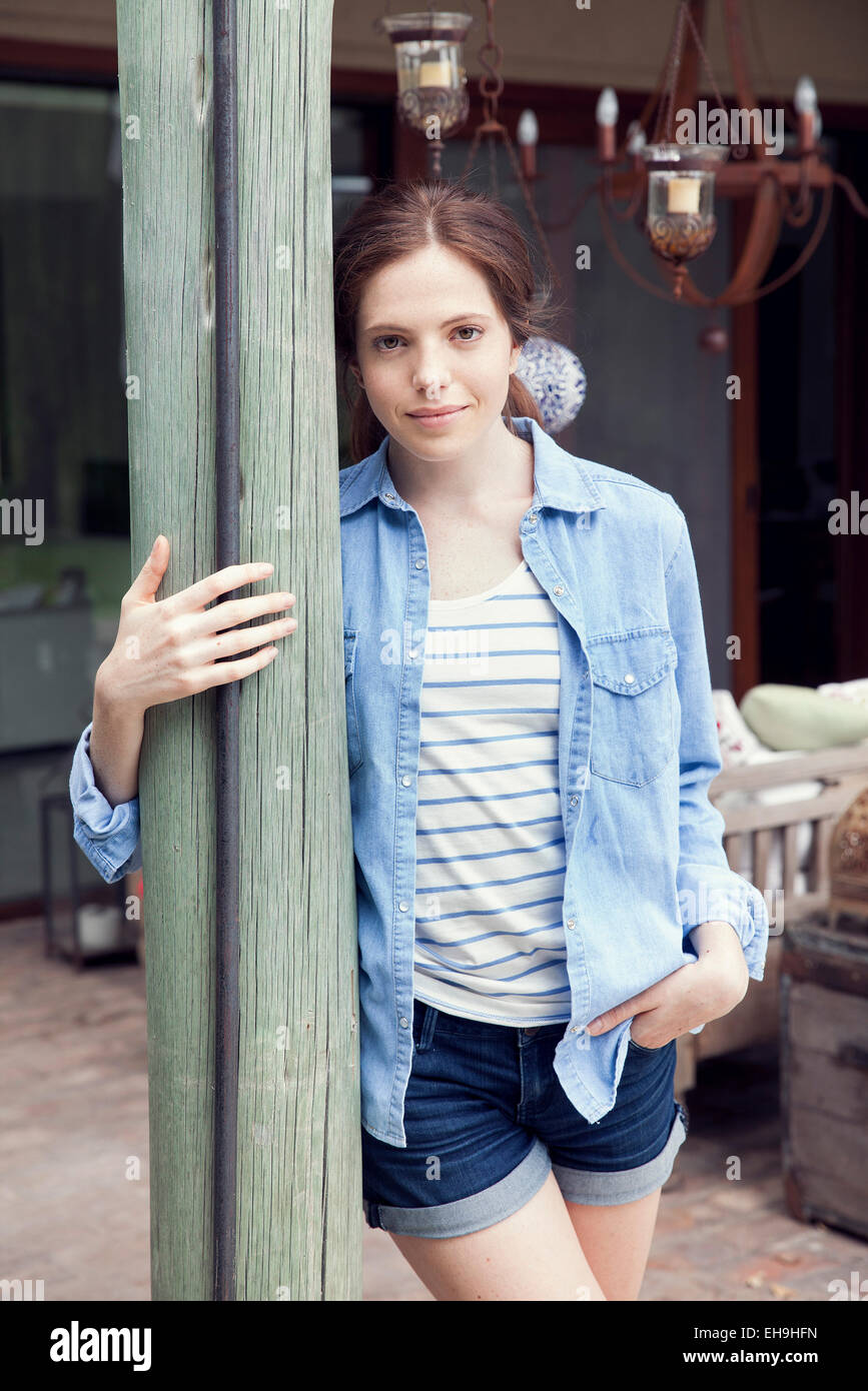 Young woman leaning against wooden post, portrait Stock Photo - Alamy