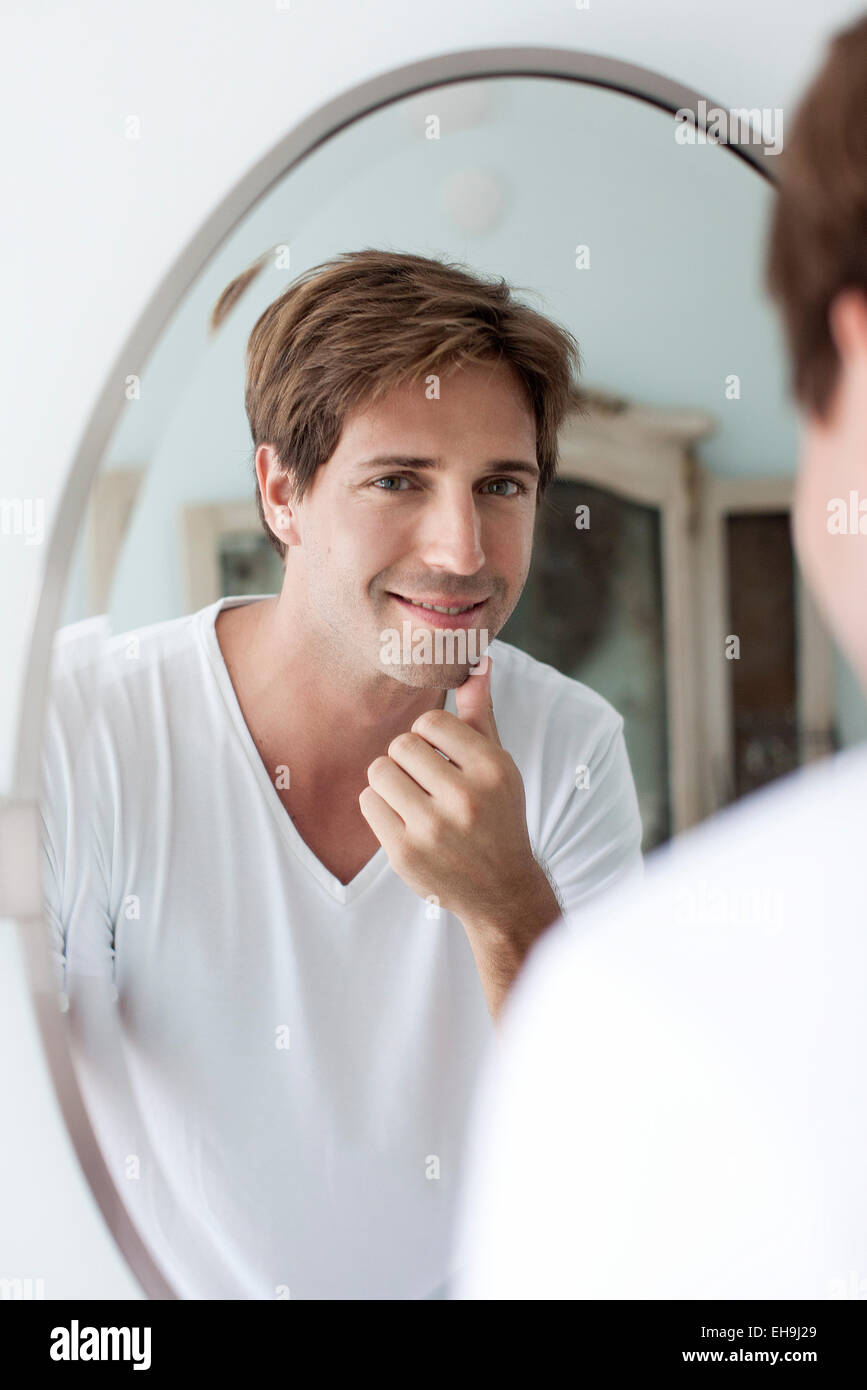 Man looking at self in mirror touching facial stubble Stock Photo - Alamy