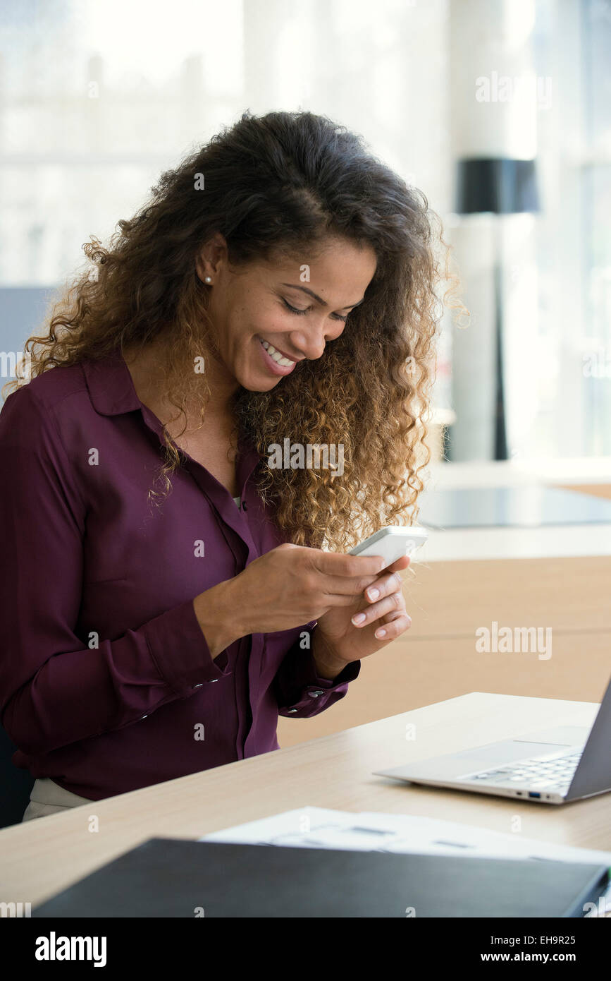 Woman text messaging with smartphone in office Stock Photo - Alamy