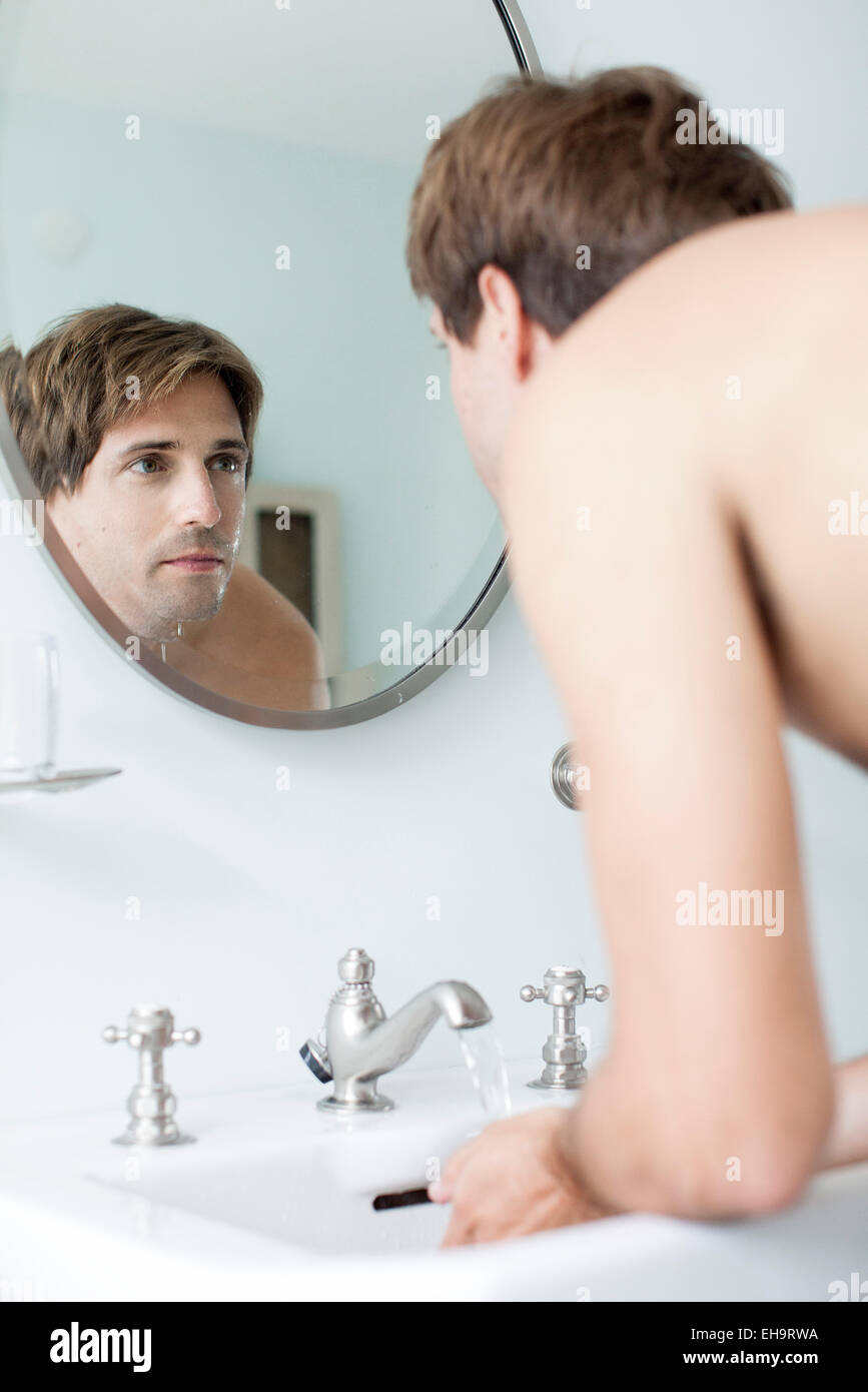 Man washing face in bathroom sink looking at self in mirror Stock Photo - Alamy
