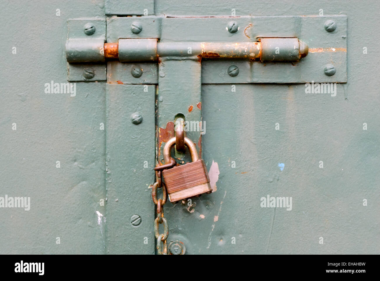 Closed rusted padlock blocking deadbolt on green steel door Stock Photo ...