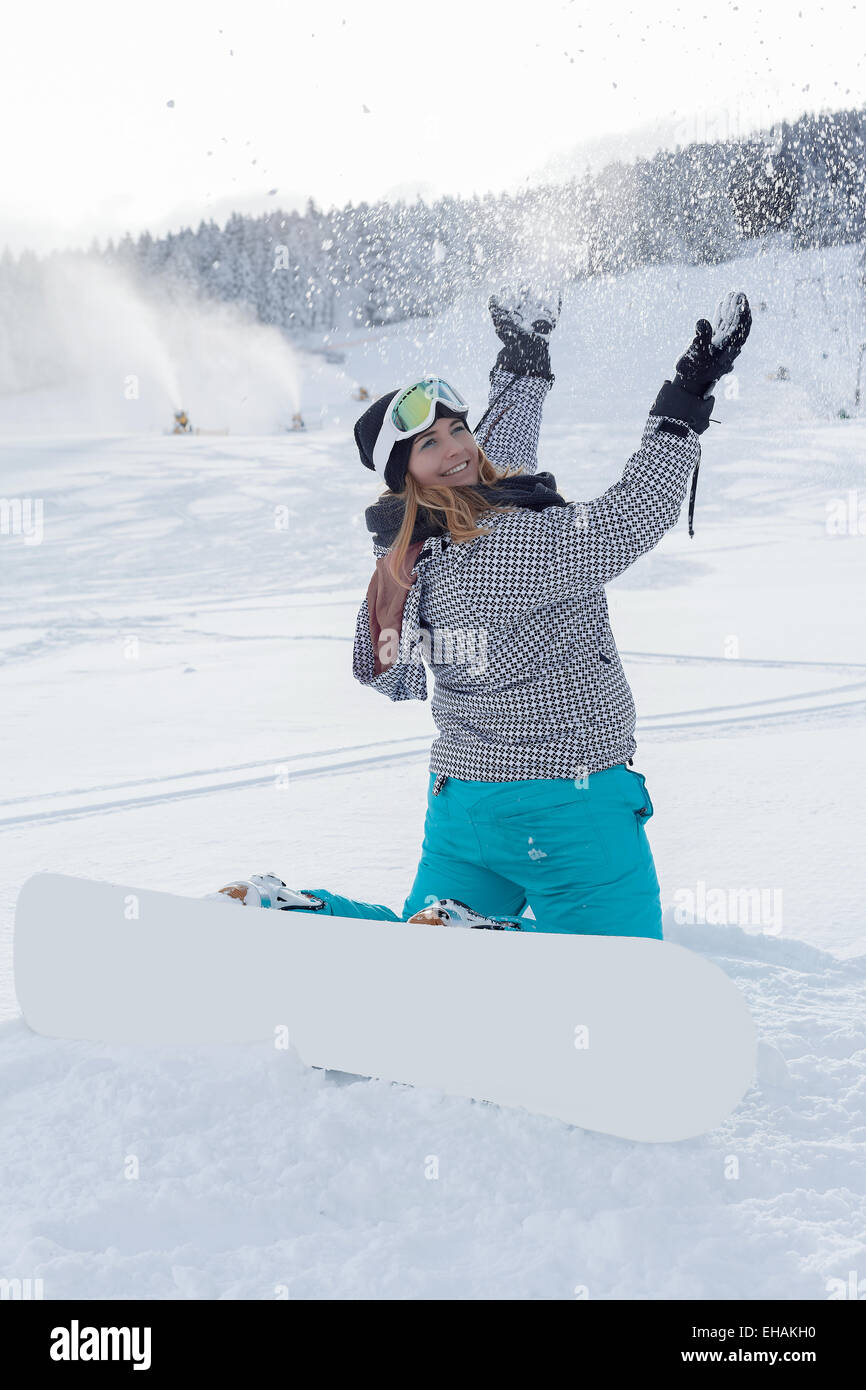 Young, curvy girl with snowboard, kneeling on the ski slopes throwing ...