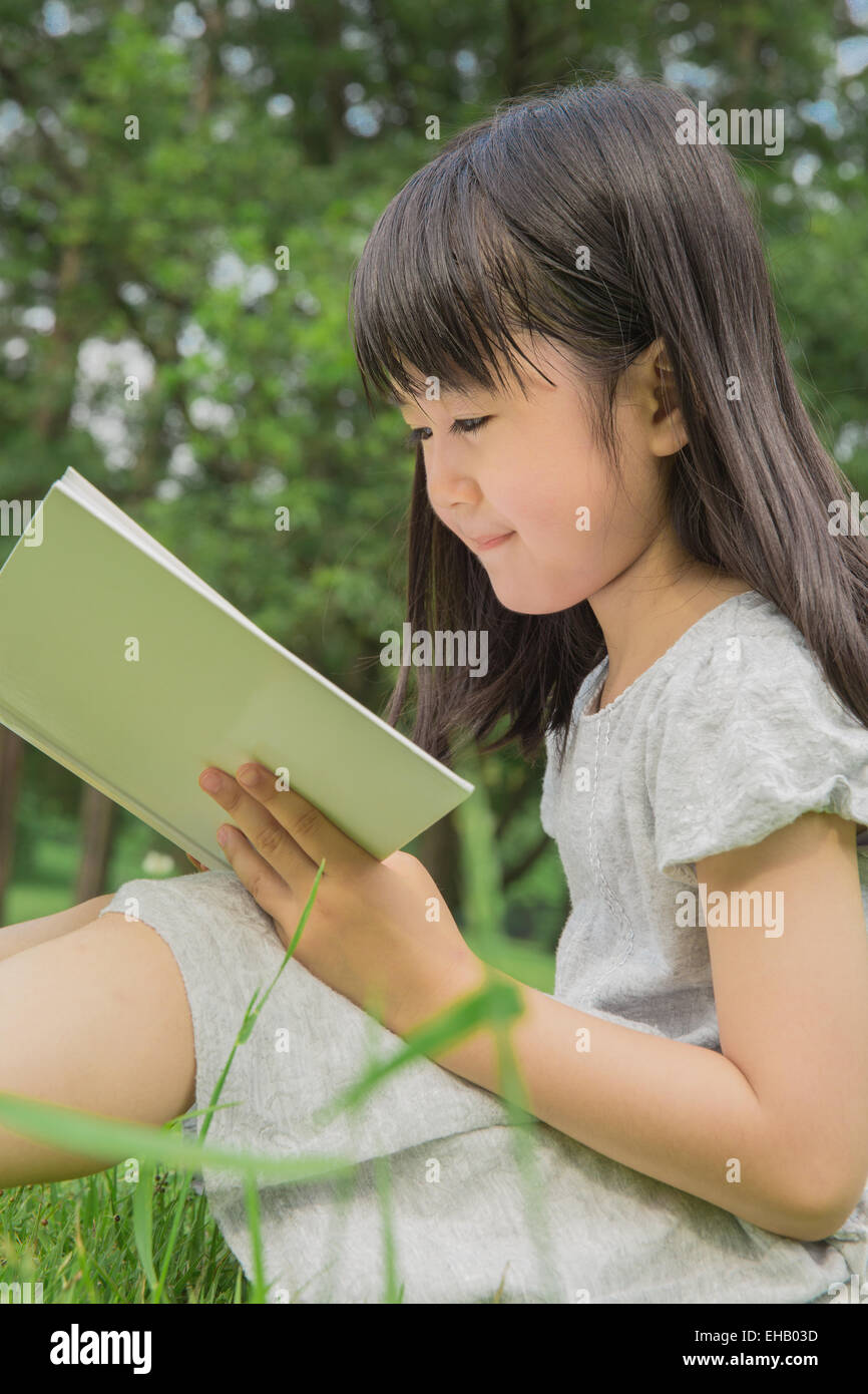 Japanese kid sitting on grass with a book in a park Stock Photo - Alamy