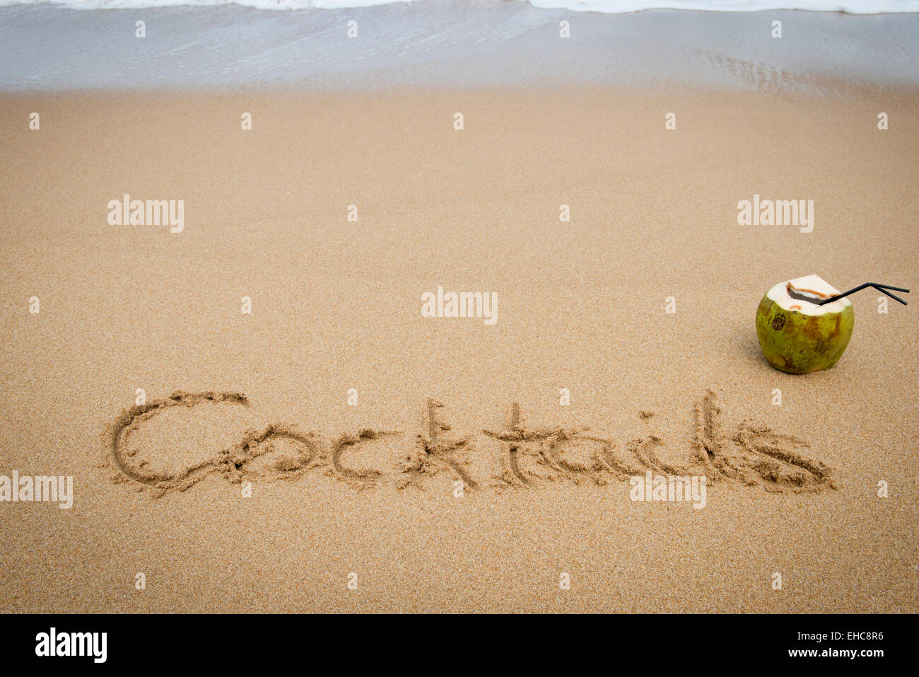 The word cocktails written in the sand on a beach, with a coconut ...