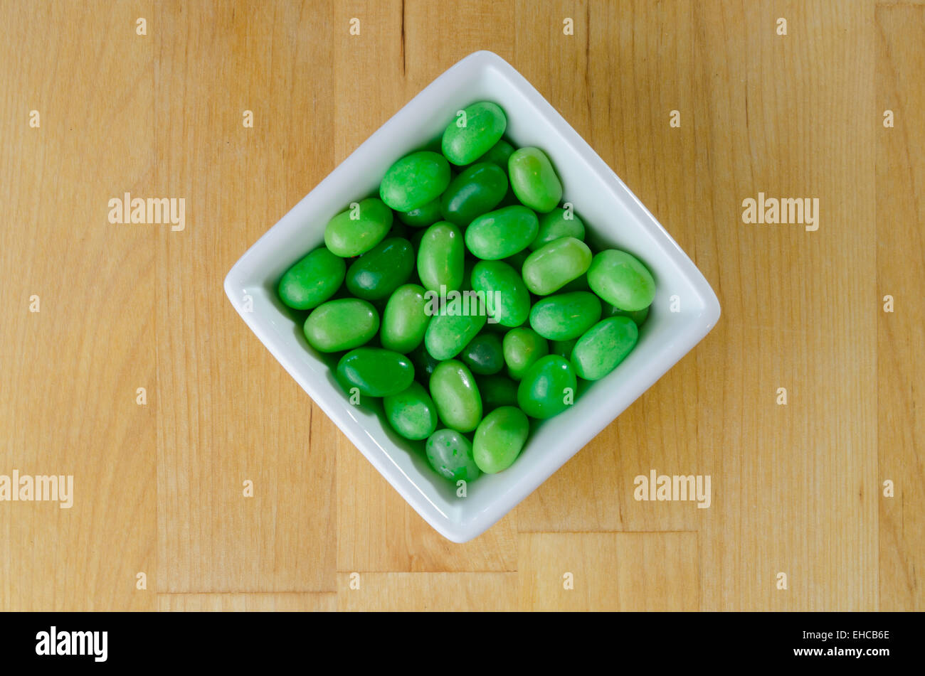 A pile of green jelly beans in a white bowl against a butcher block ...