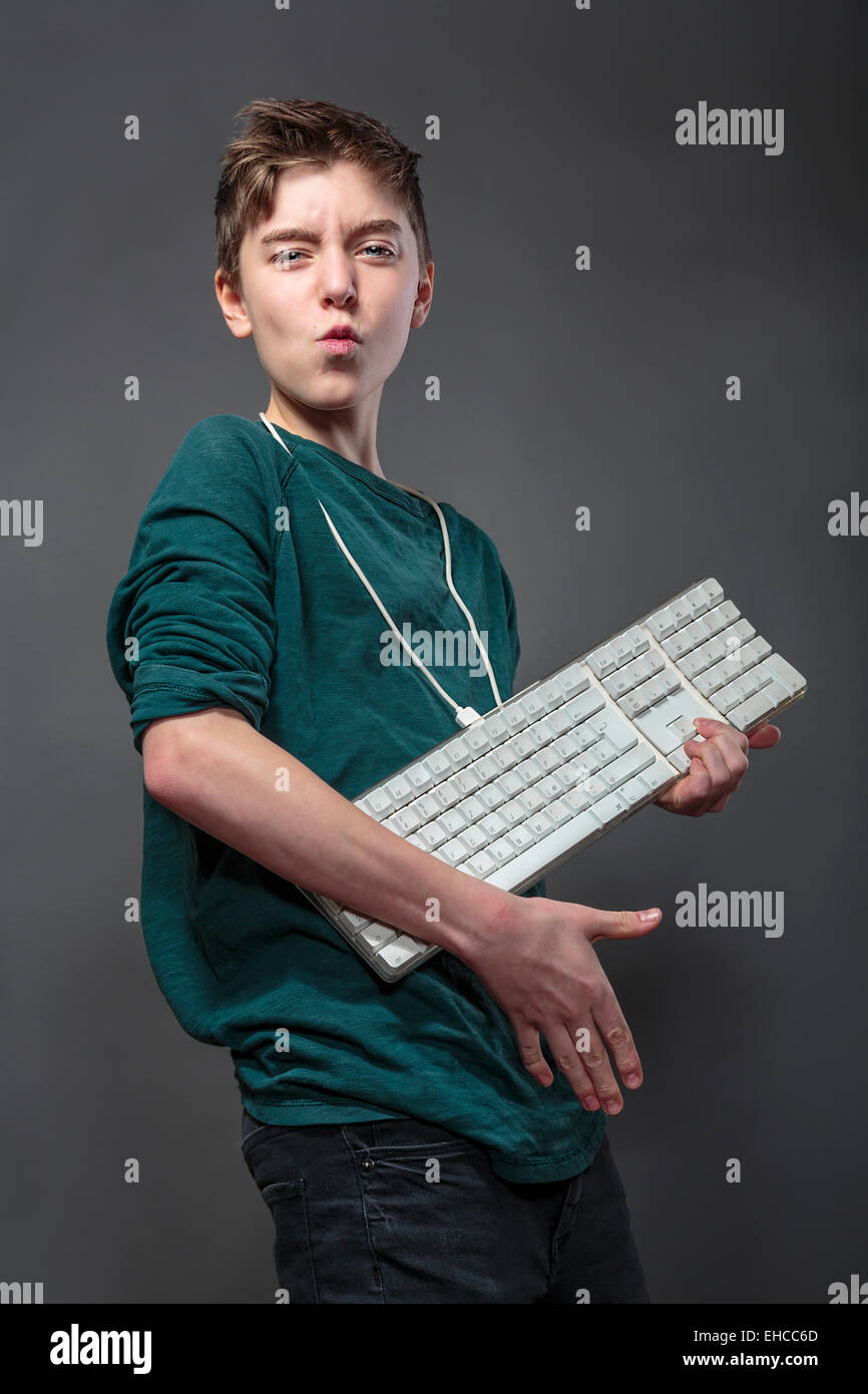 teenage boy using a computer keyboard like a guitar, isolated on gray ...