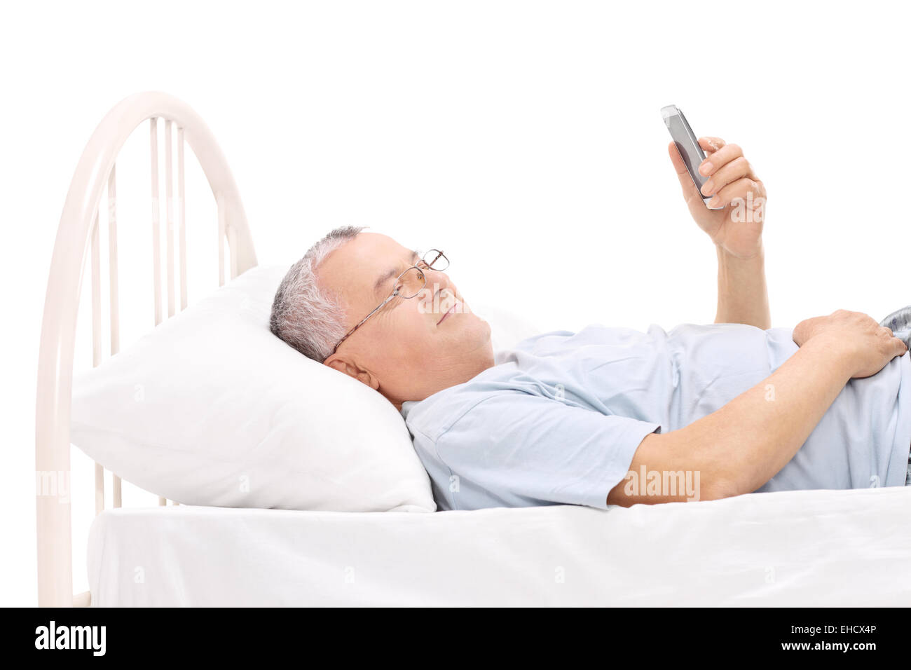 Senior watching something on his cell phone in bed isolated on white ...