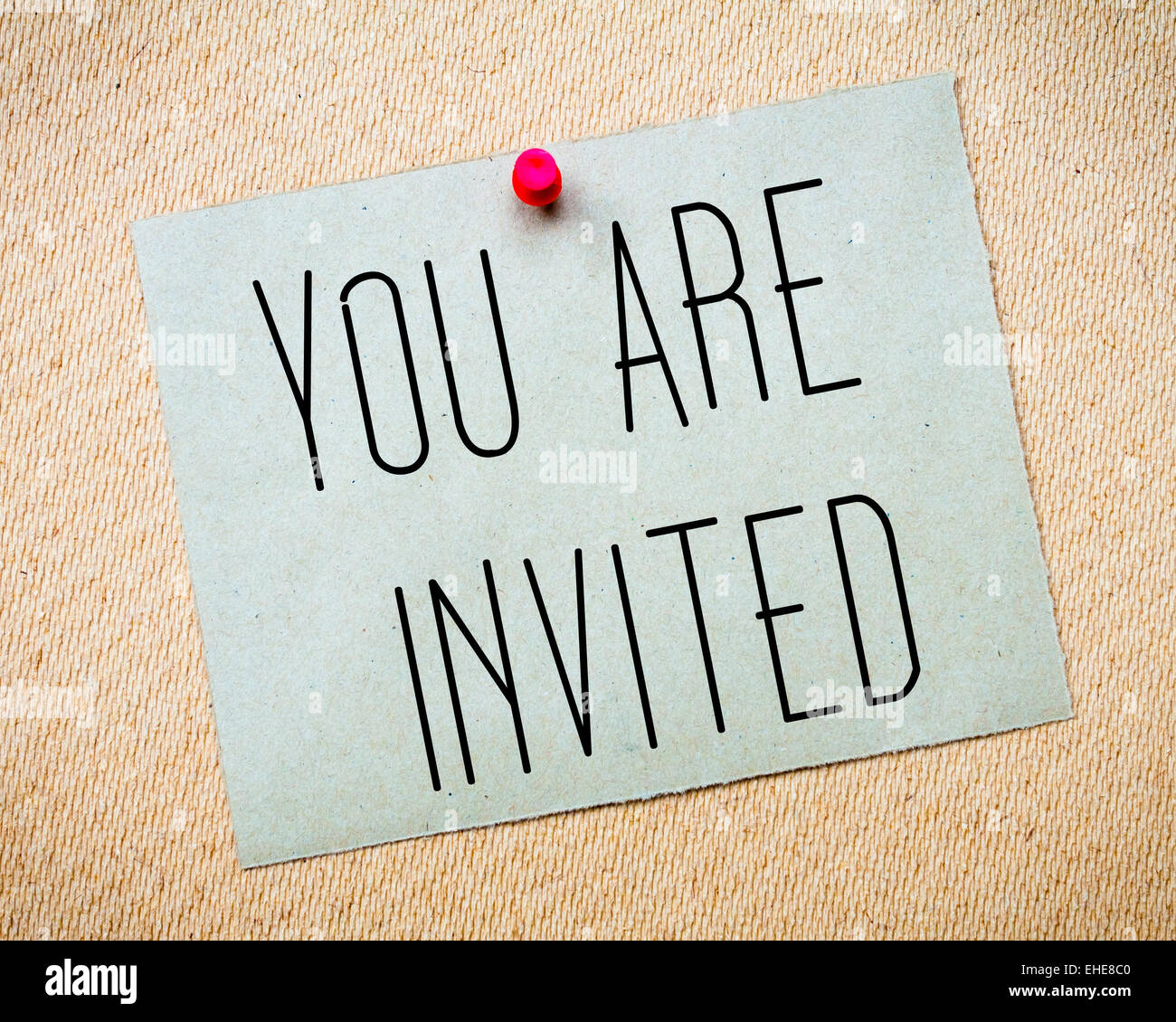 Recycled paper note pinned on cork board. You Are Invited Message ...