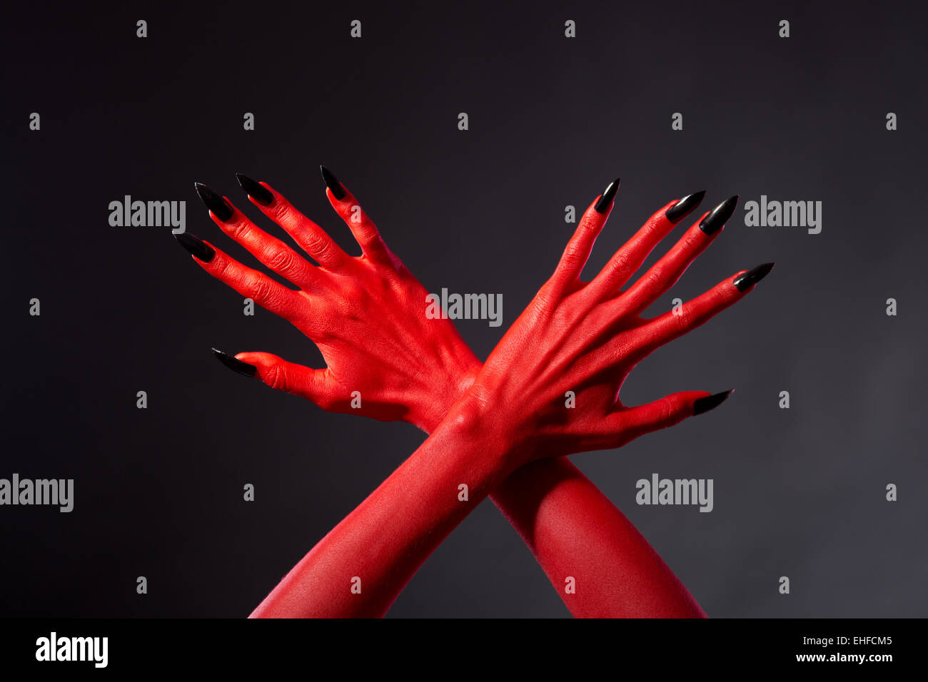 Crossed red devil hands with black nails, studio shot on black ...