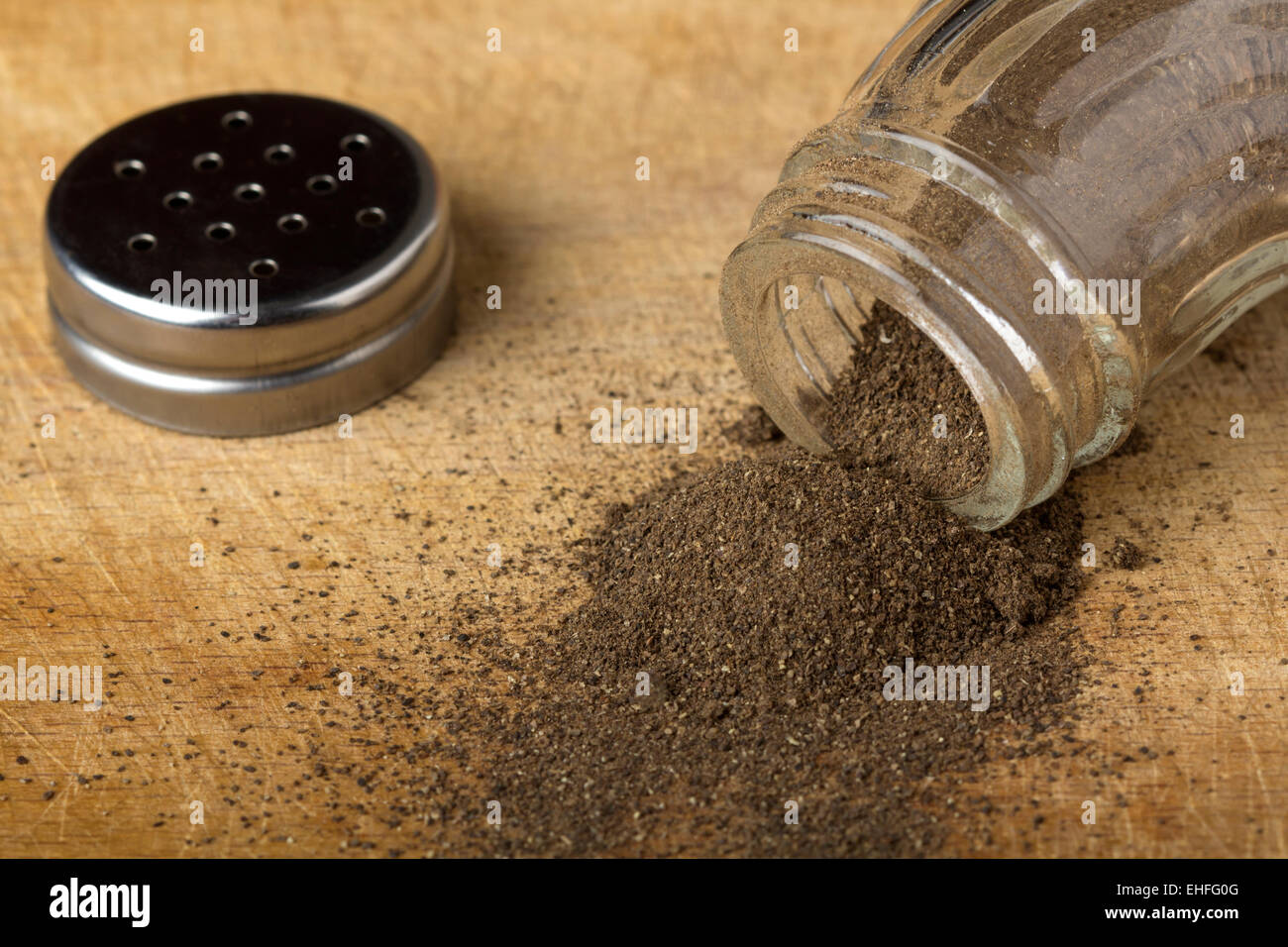 Traditional glass pepper cellar and spilled pepper on a wood background ...
