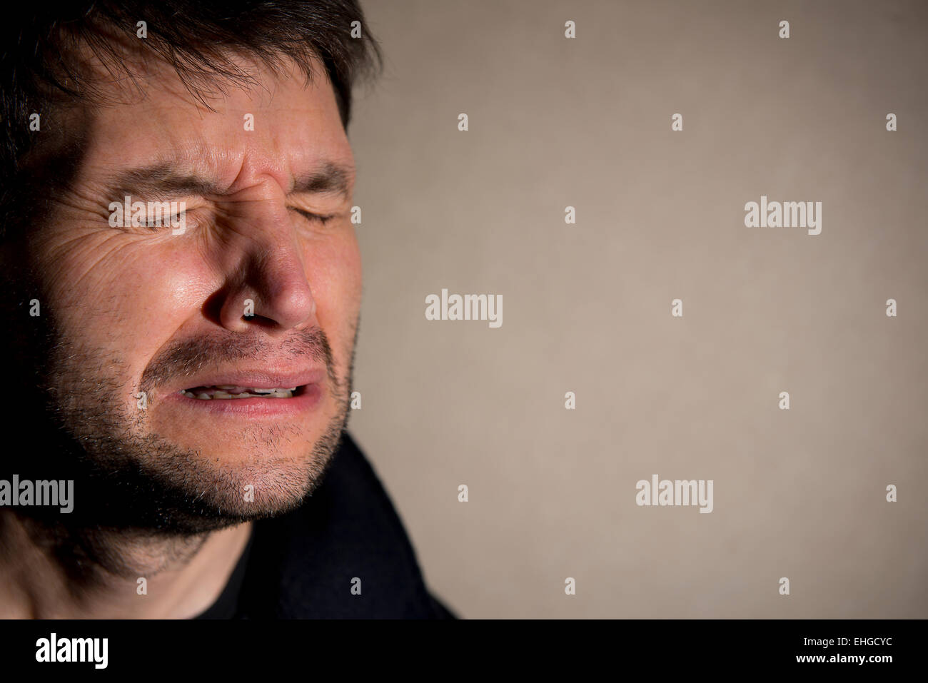 Close up of unshaven man, his eyes are closed and tearful, suffering ...