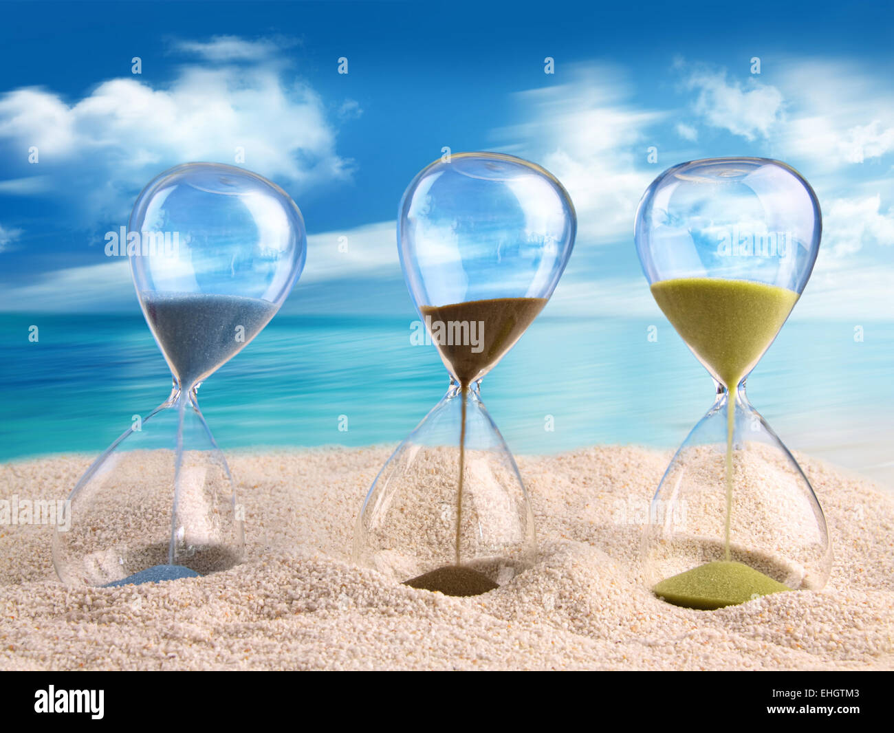 Three hourglass in the sand with blue sky Stock Photo - Alamy